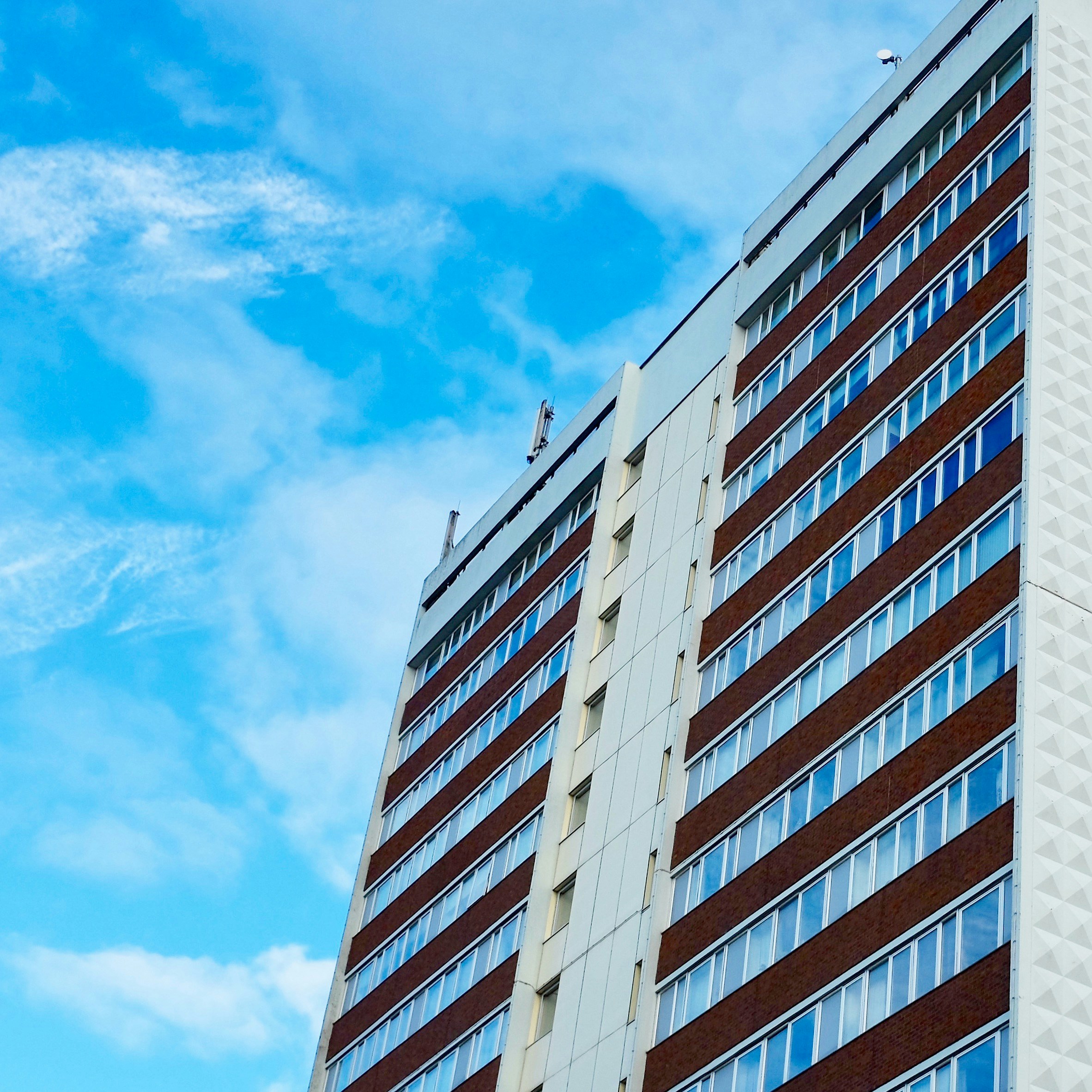 Modern building facade with a blend of brick and glass, set against a vibrant blue sky with wispy clouds.