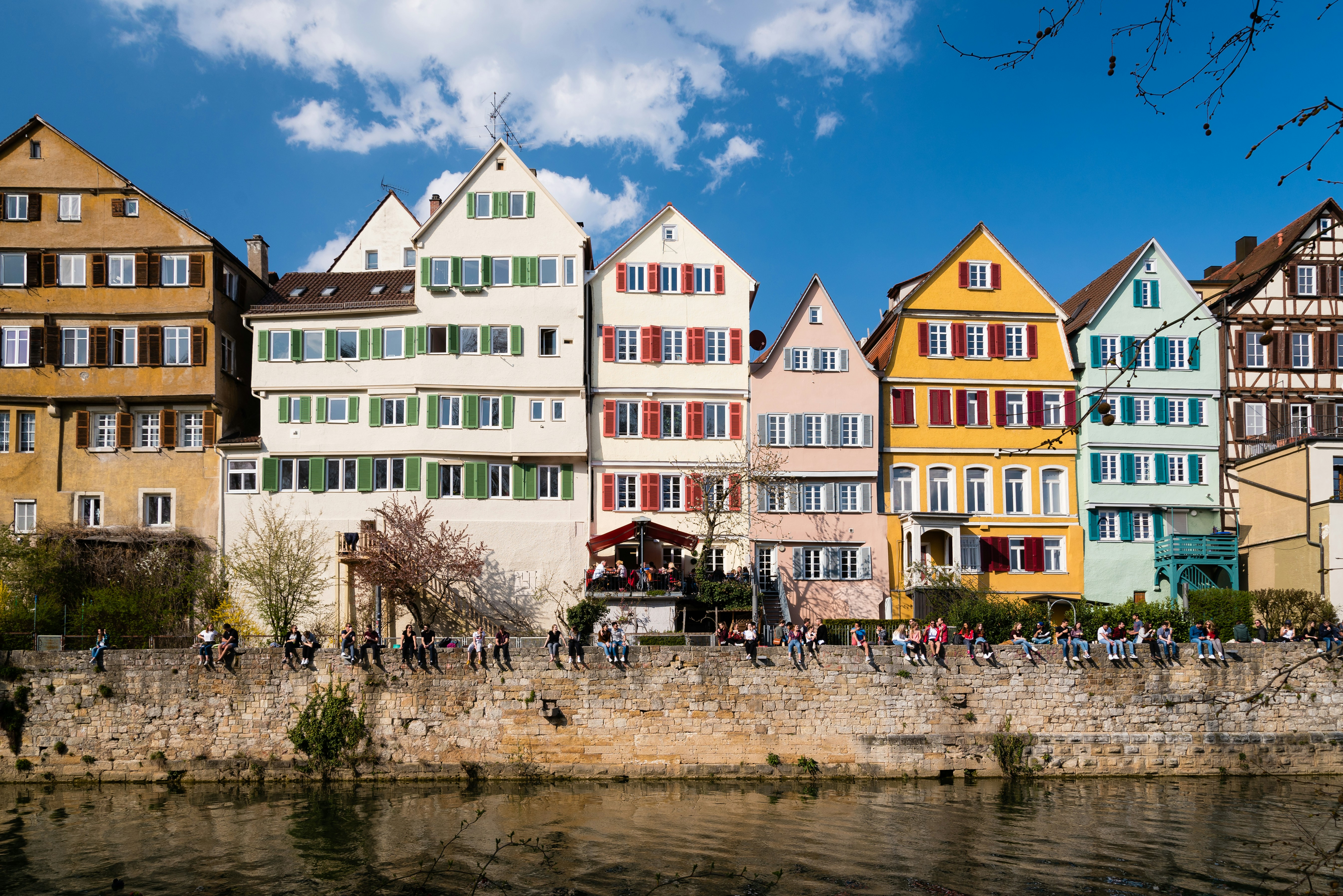 Colorful historic buildings line the riverbank under a bright blue sky.
