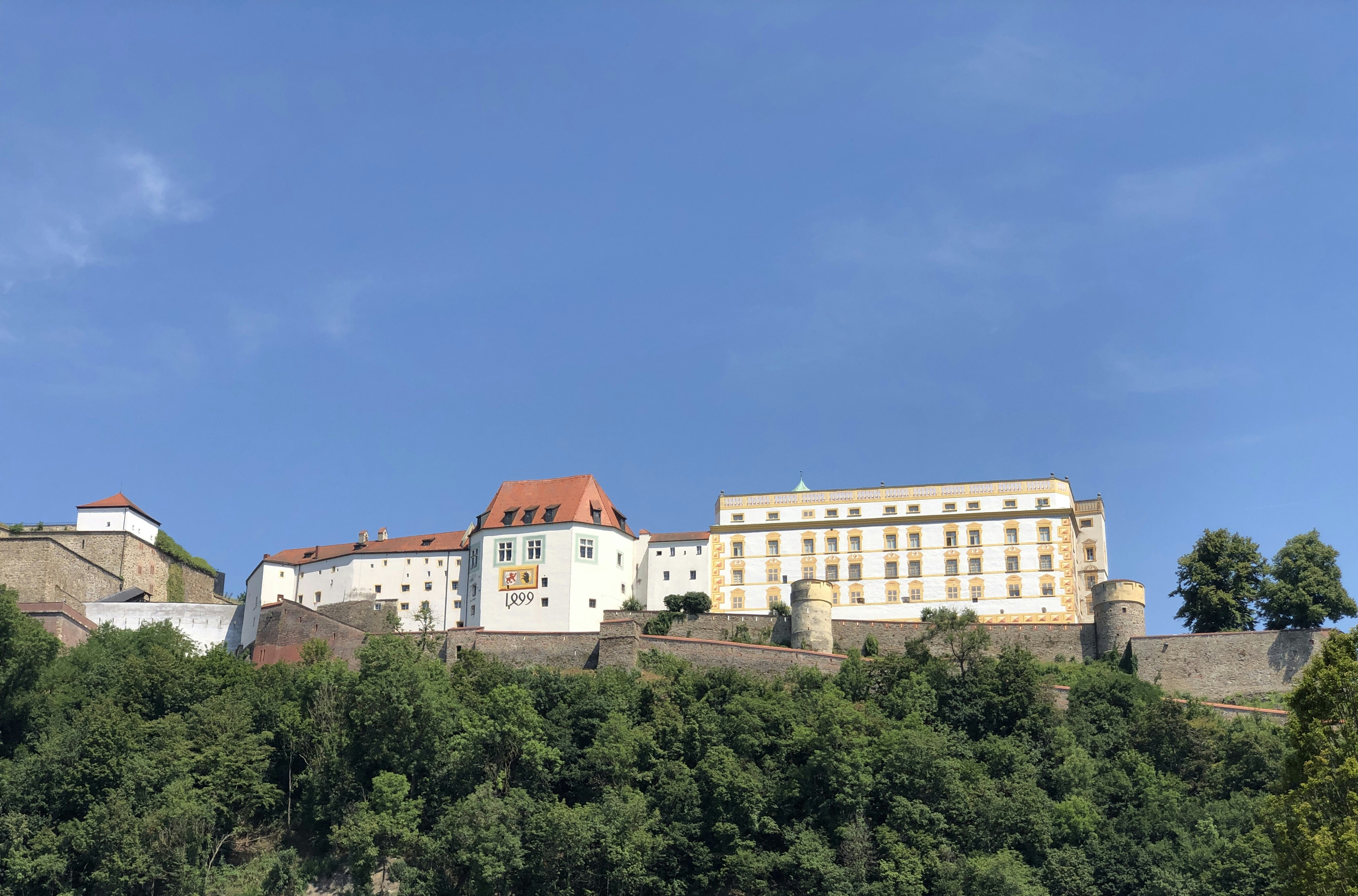 Historic buildings perched atop a lush, green hillside under a clear blue sky.