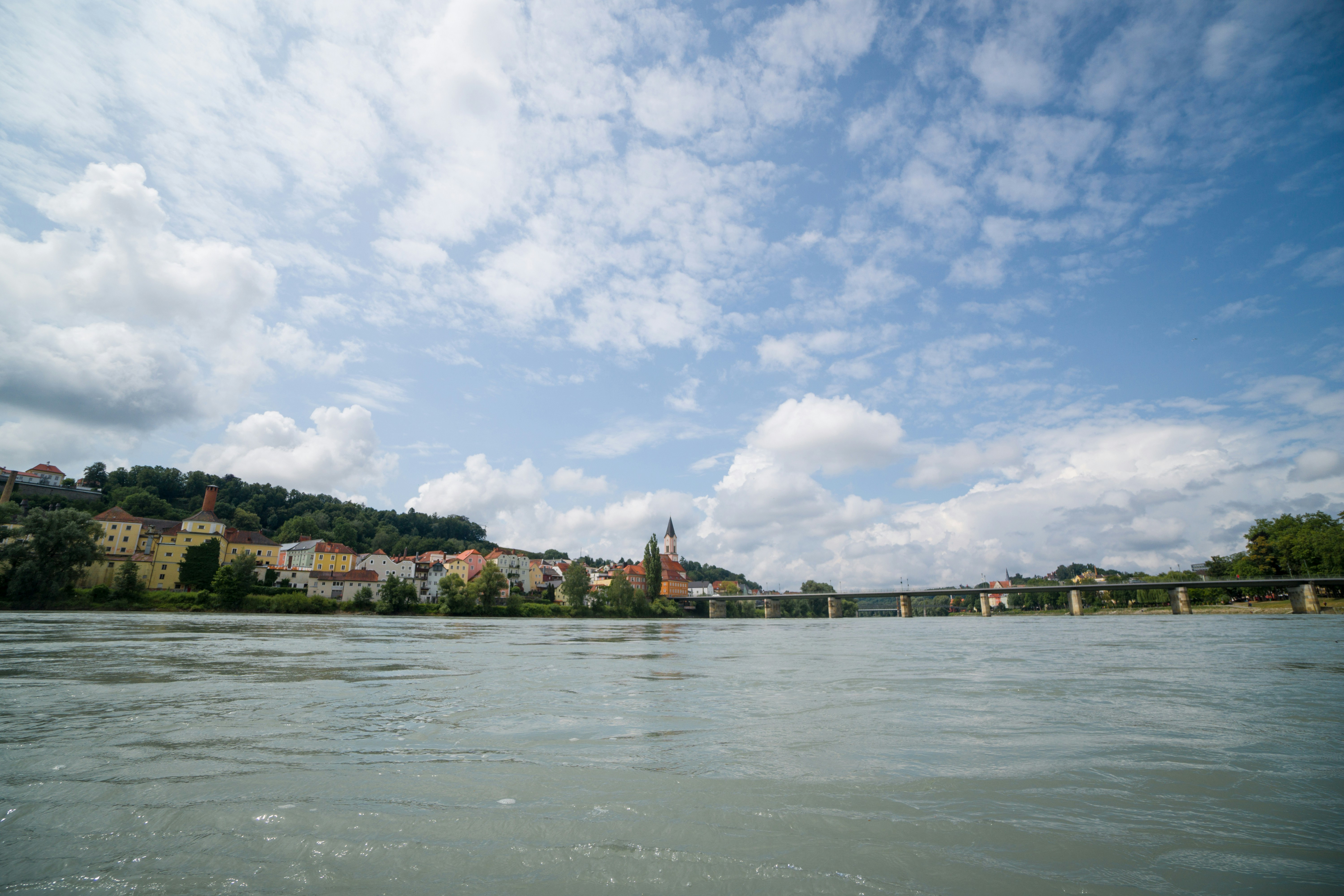 Idyllic riverside town with a prominent church tower under a vibrant sky of scattered clouds.