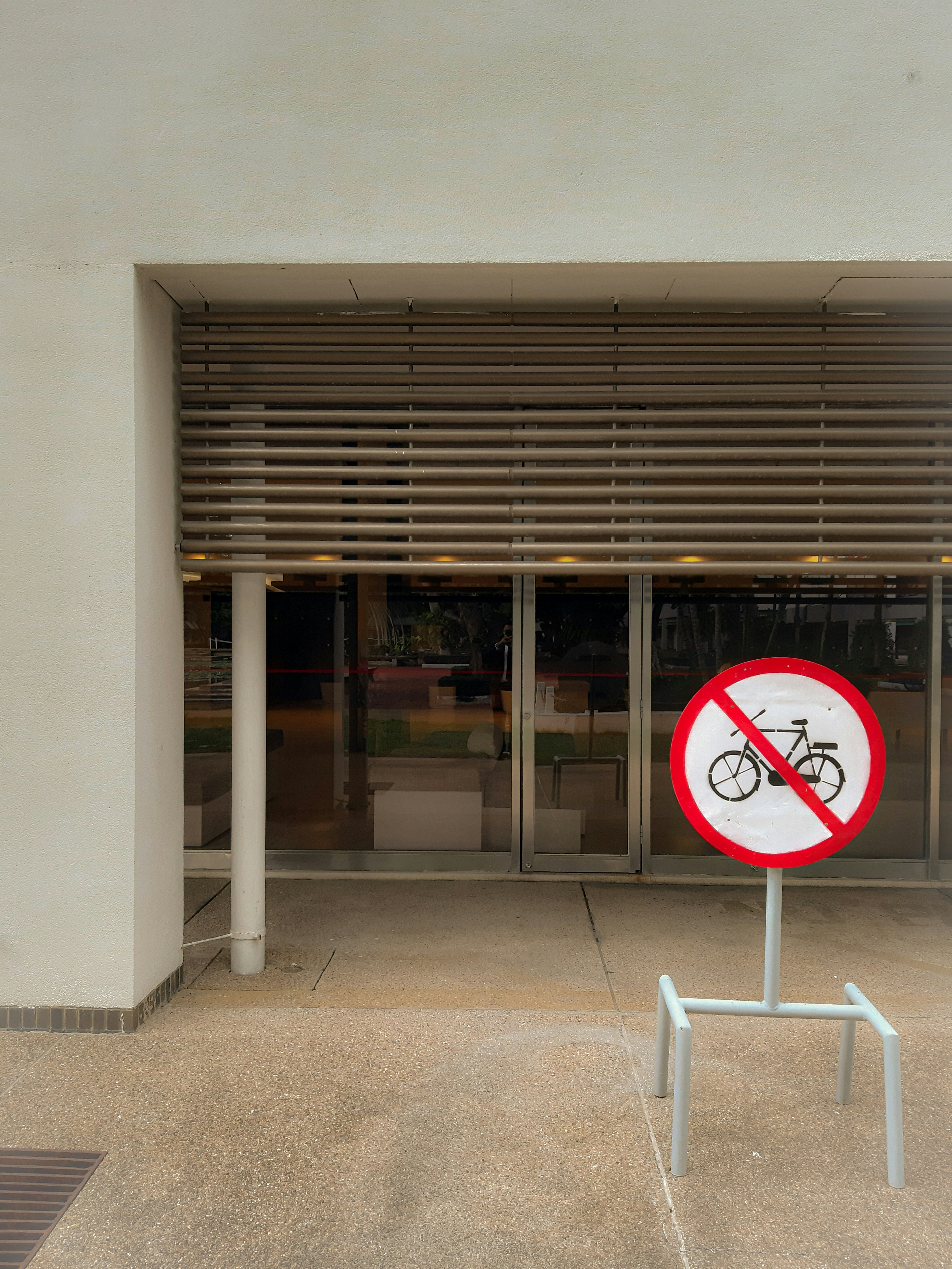 No bicycles allowed sign stands prominently in front of a modern building with horizontal slats and glass facade.