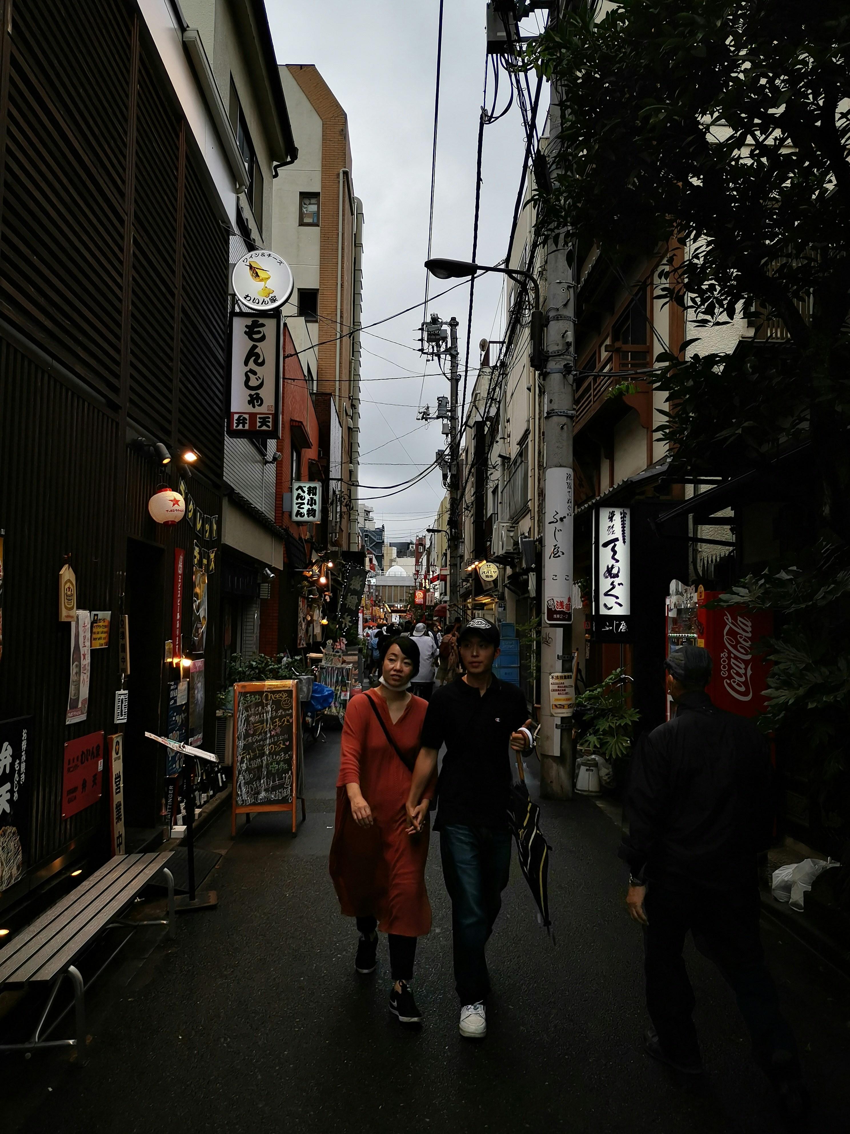 Couple walking hand-in-hand through a bustling alleyway adorned with vibrant shop signs and lanterns. The atmosphere captures the essence of urban life.