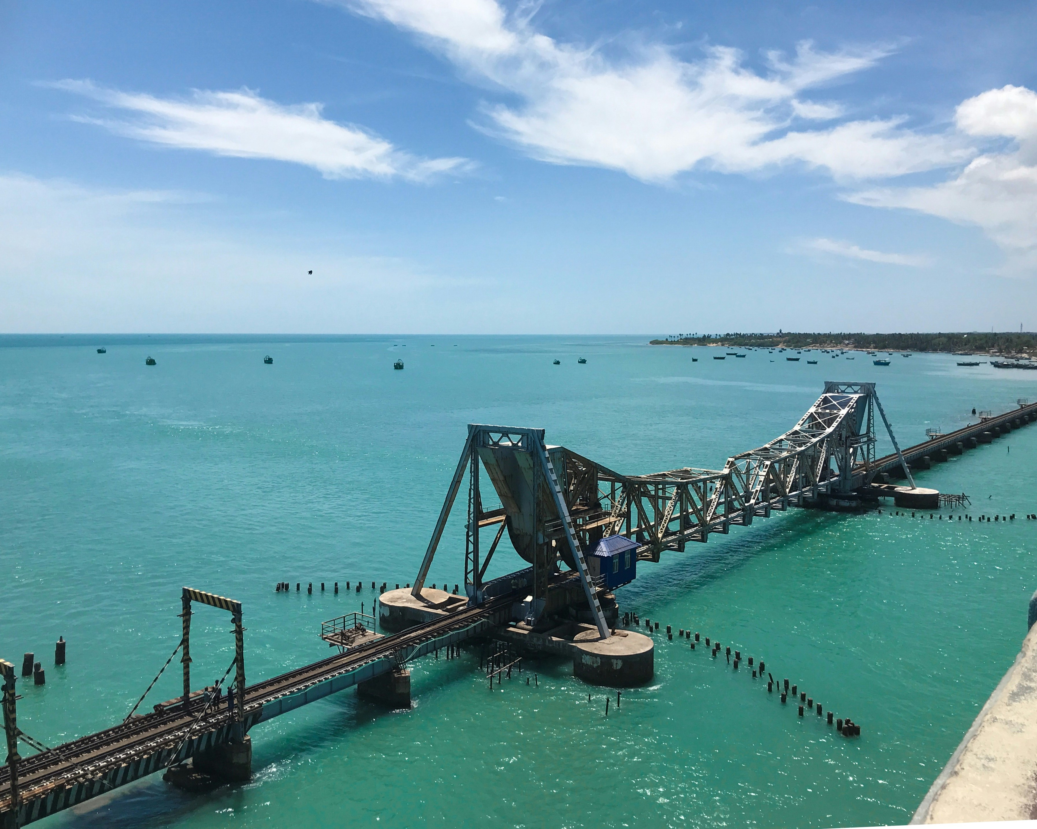 Aerial view of a cantilever bridge spanning vibrant turquoise waters under a partly cloudy sky.