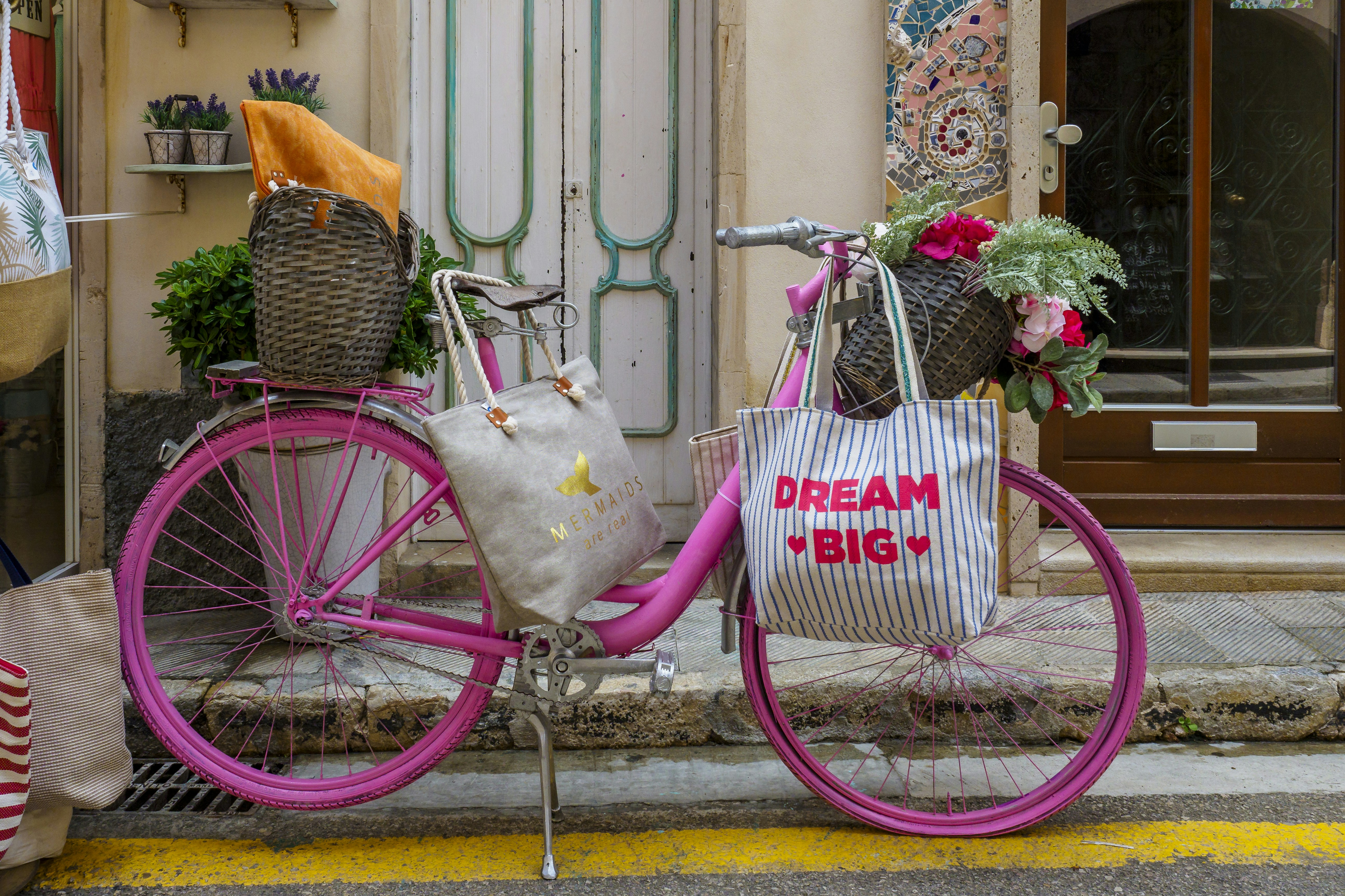 Pink bicycle adorned with baskets and bags, set against a decorative doorway.