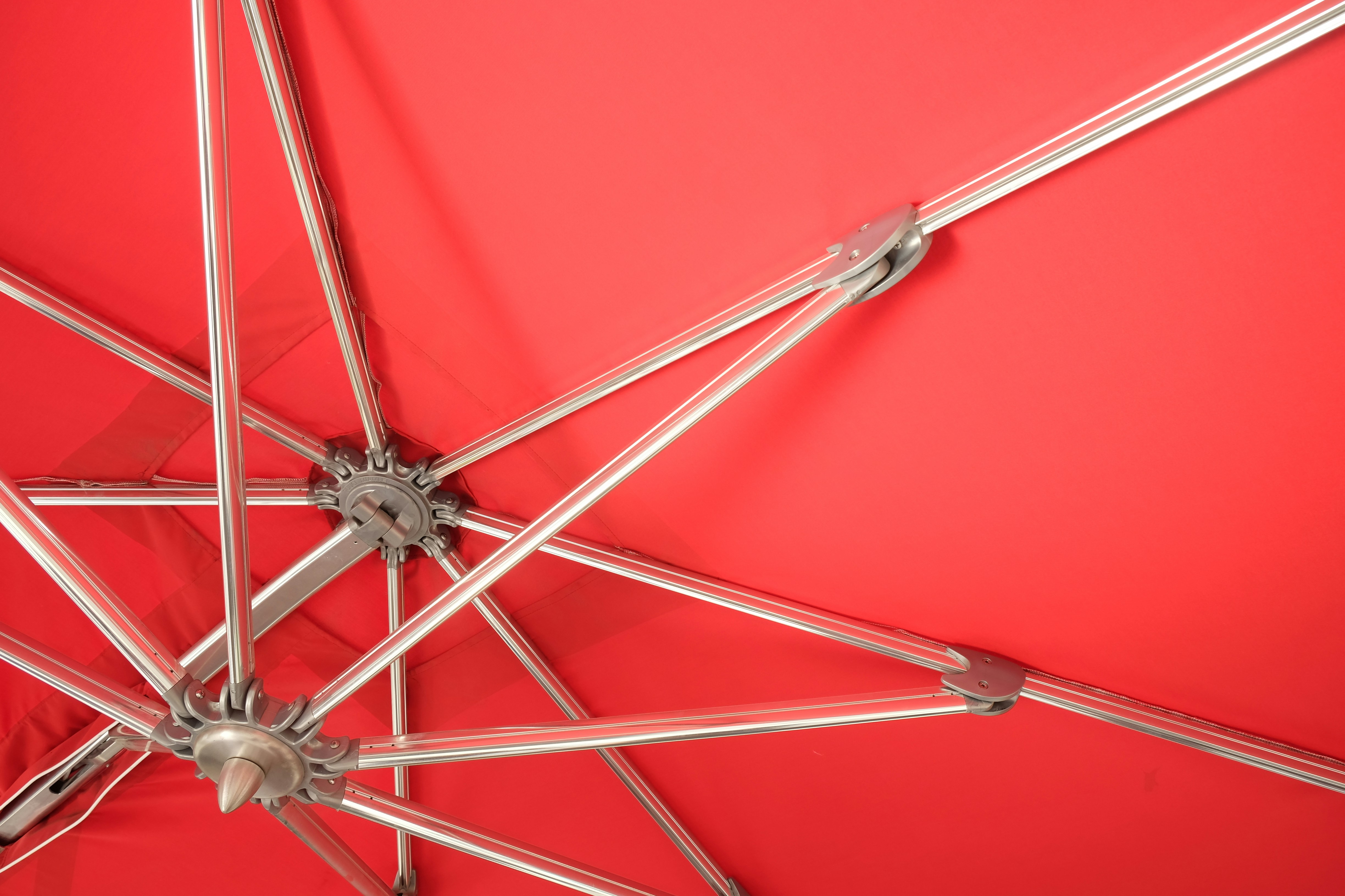 Intricate framework of a red umbrella showcasing its structural design and engineering. The interplay of metal and fabric creates a visually striking pattern.