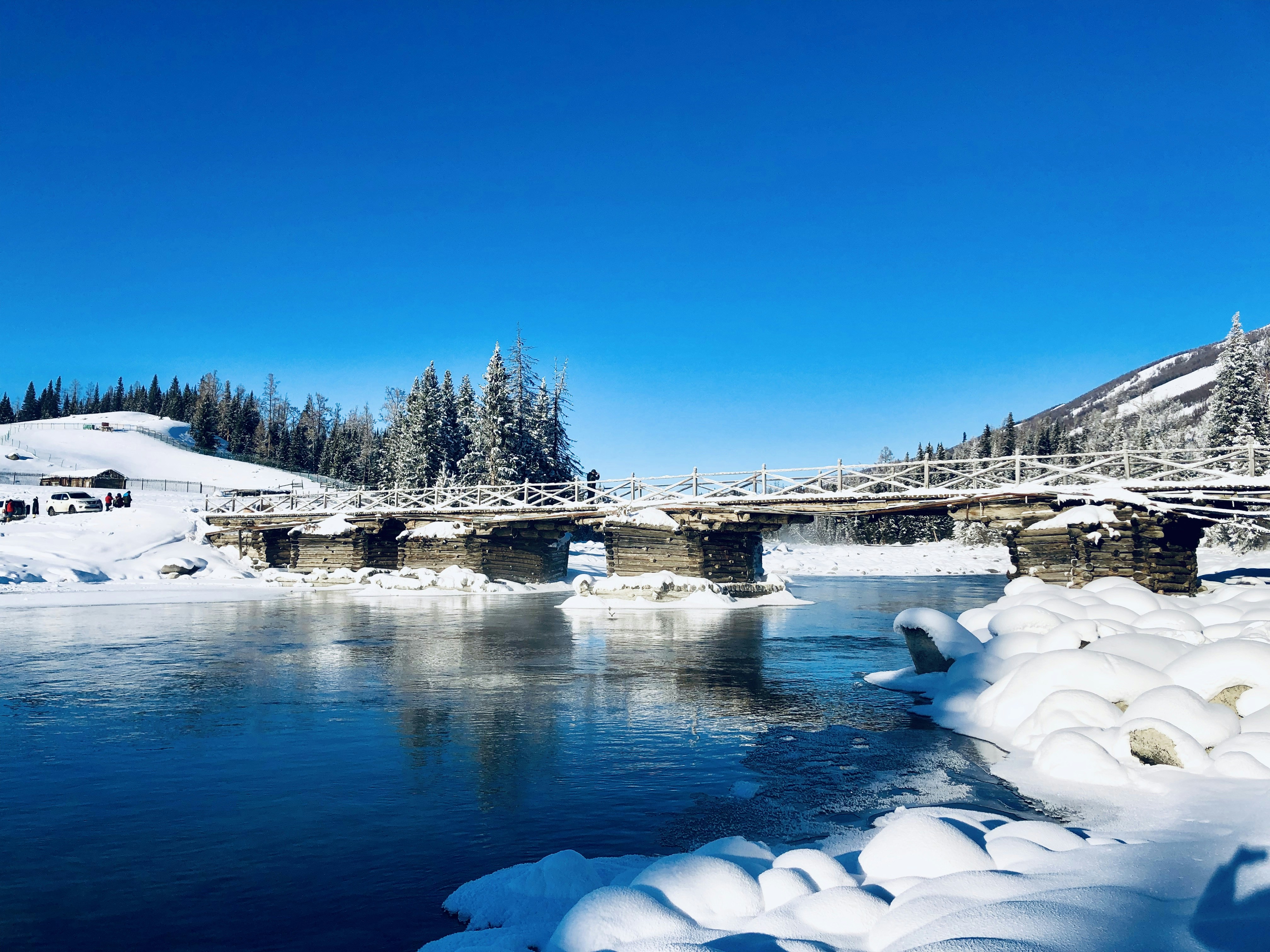 Snow-covered bridge spans a serene, icy river under a clear blue sky.