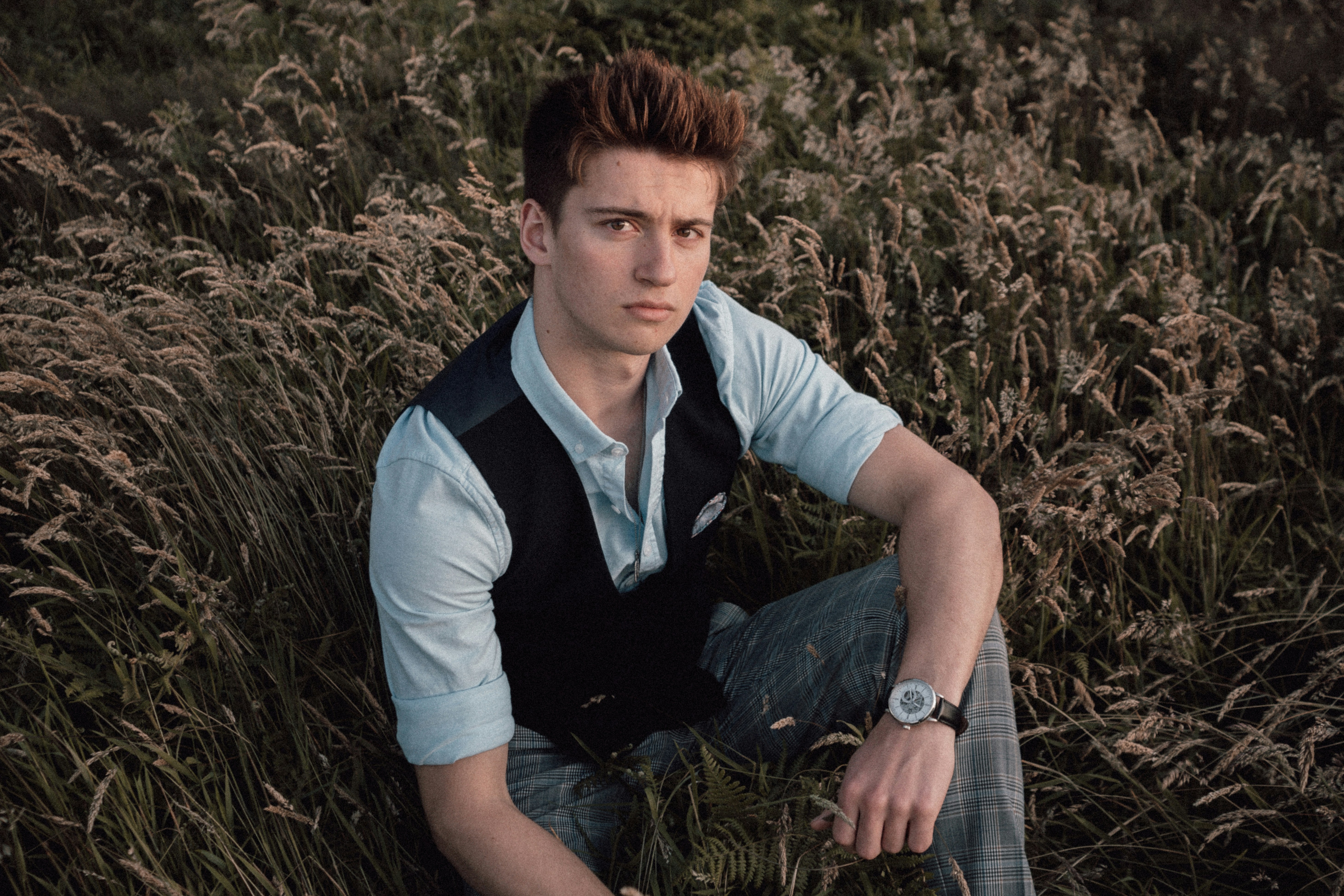 Person seated in a field of tall grasses, looking thoughtfully at the camera.