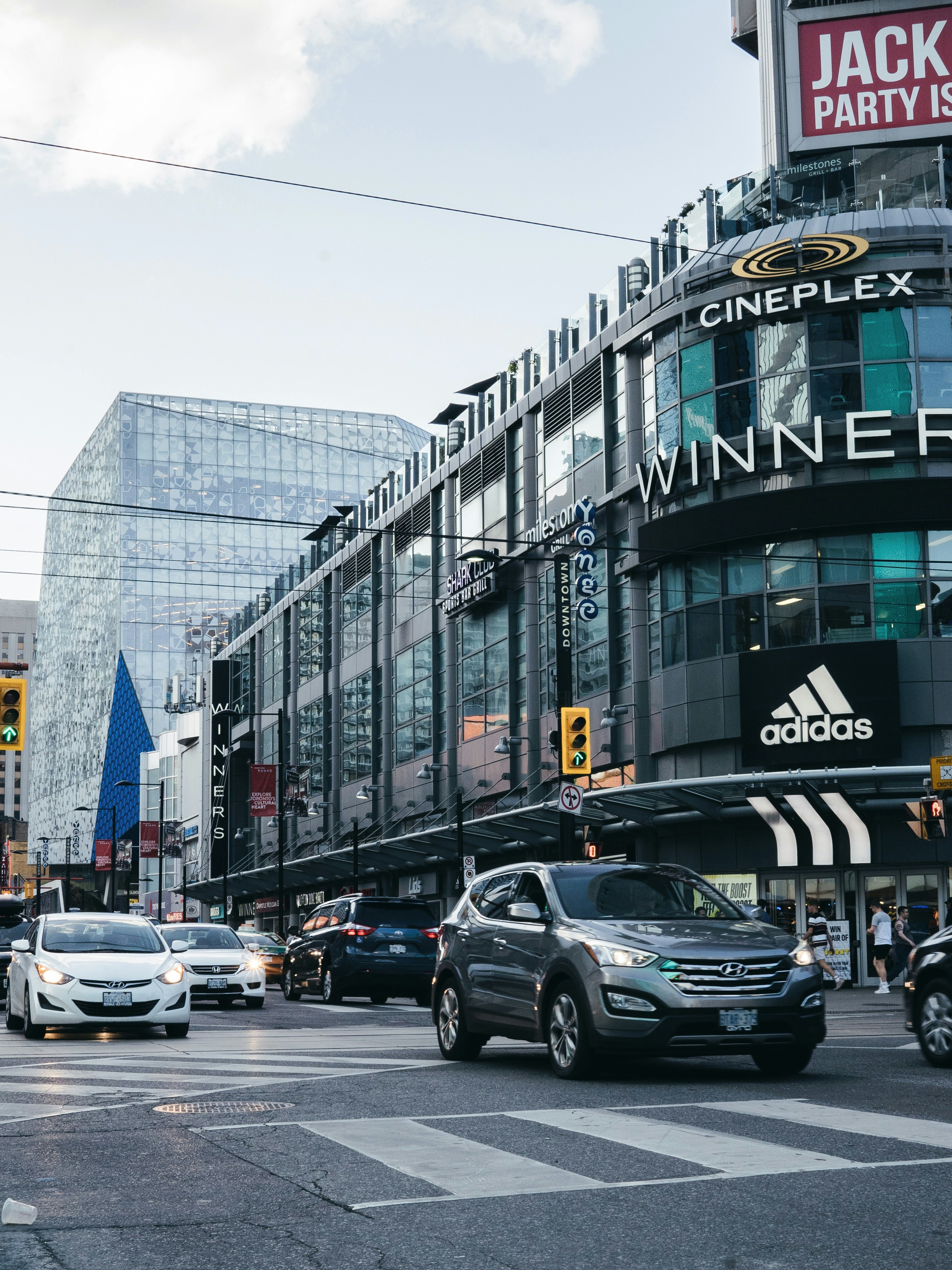 Busy urban intersection featuring modern architecture, storefronts, and a mix of vehicles in motion.