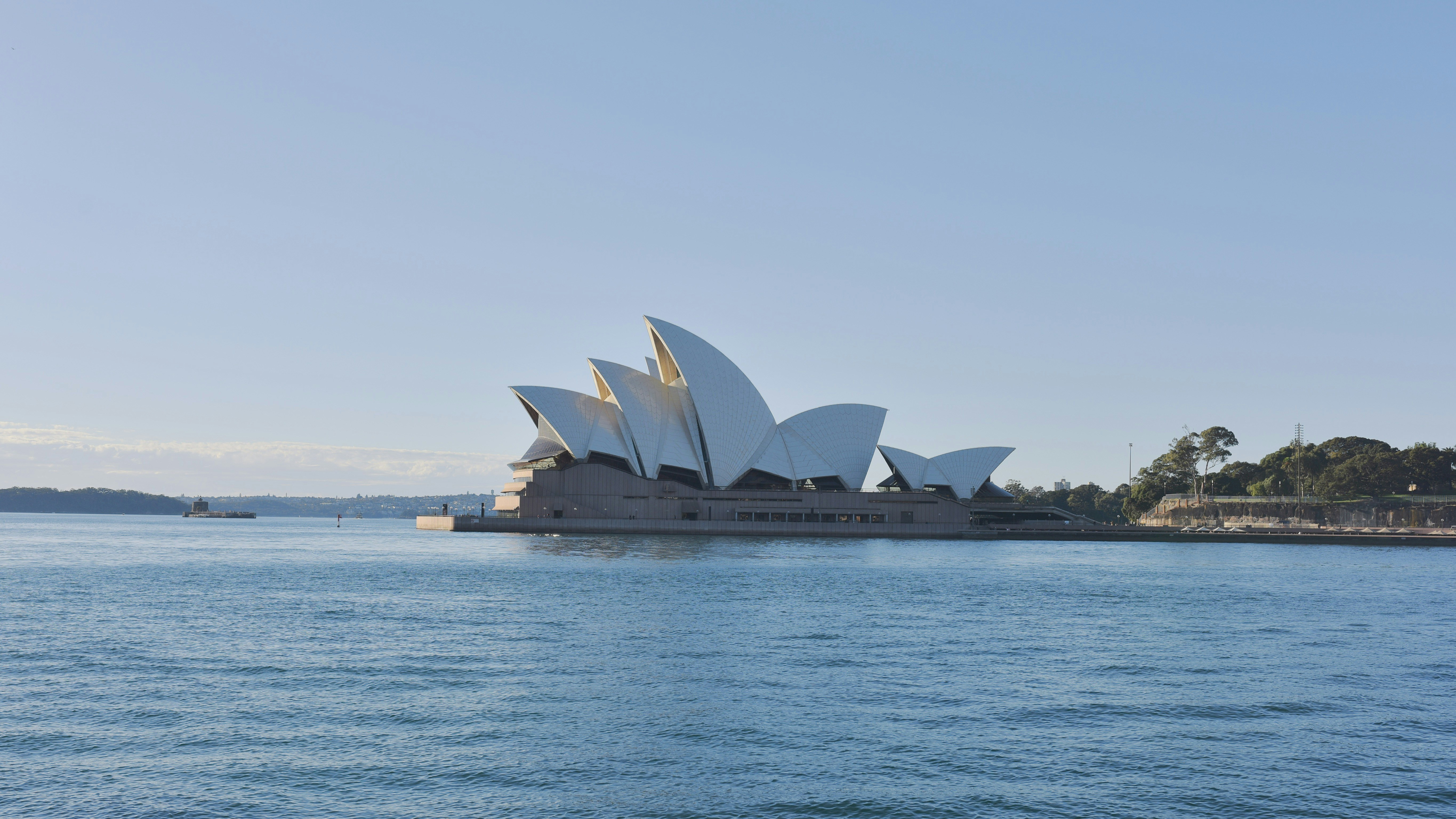 Sydney Opera House silhouetted against a clear blue sky, reflected in the calm harbor waters.