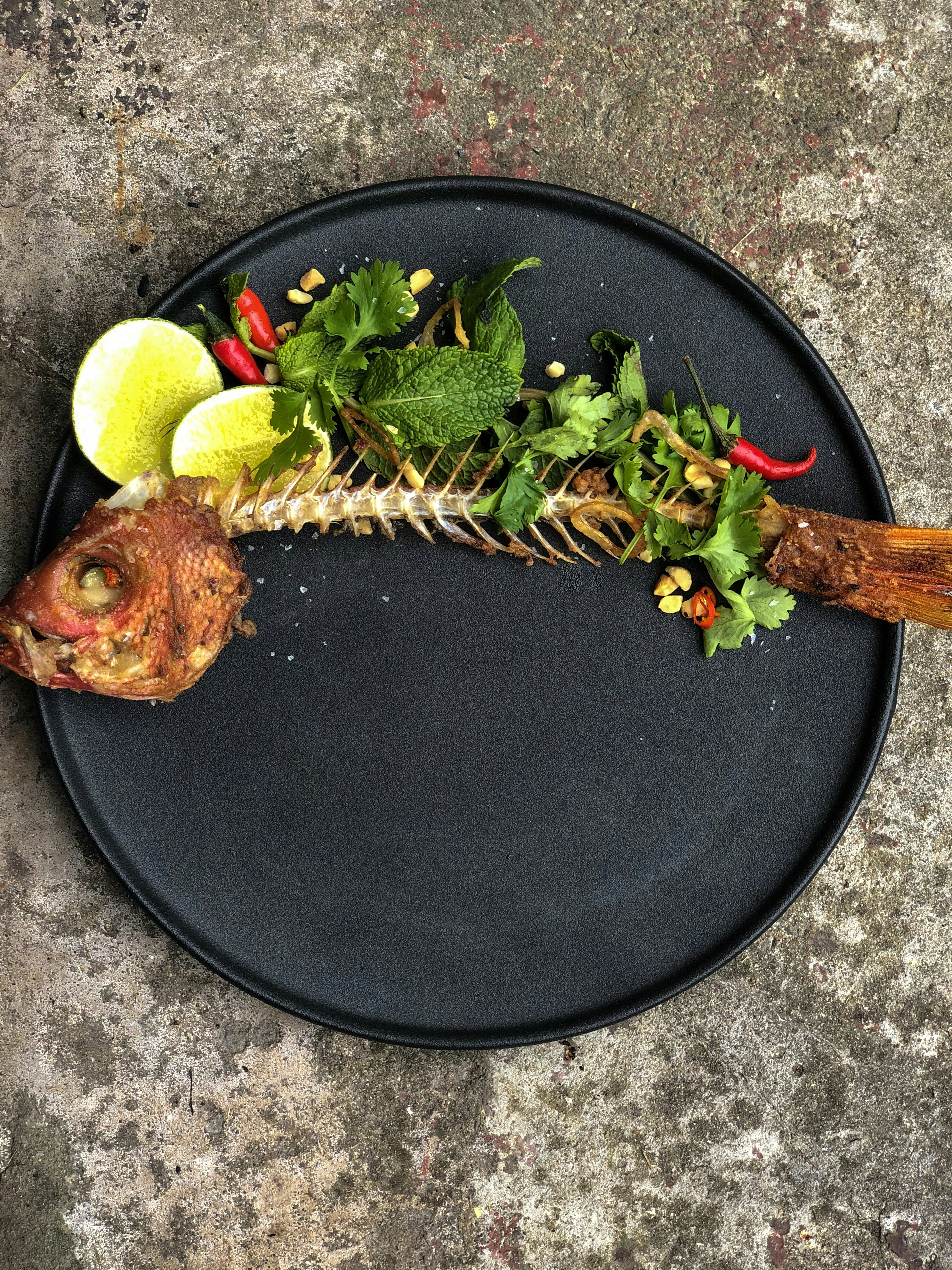 Long Skeleton of a Dish: A Crispy Head and Garnished Spine on a Matte Plate