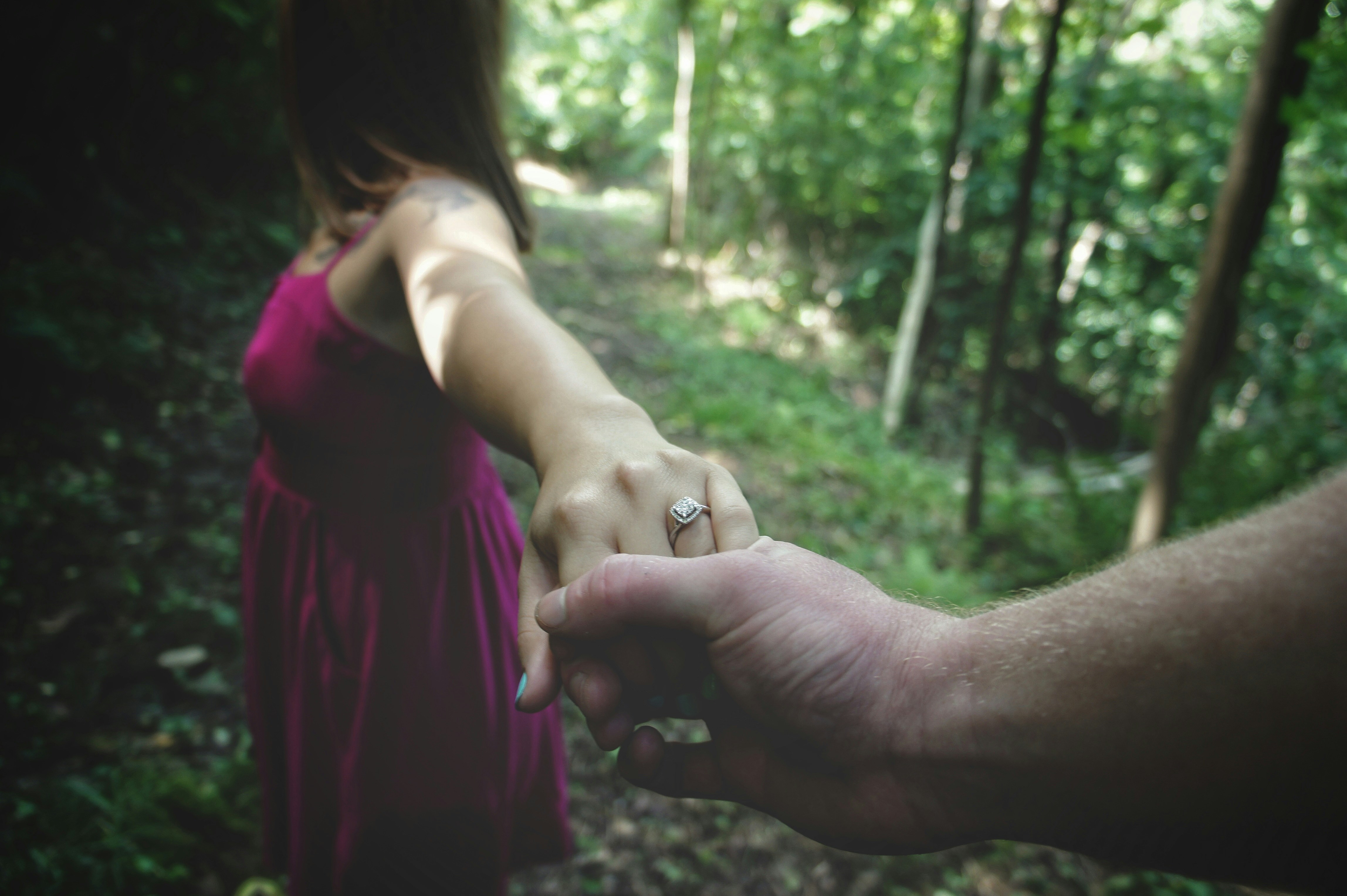 Couple holding hands while walking through a lush green forest path, conveying a sense of connection and shared experience.