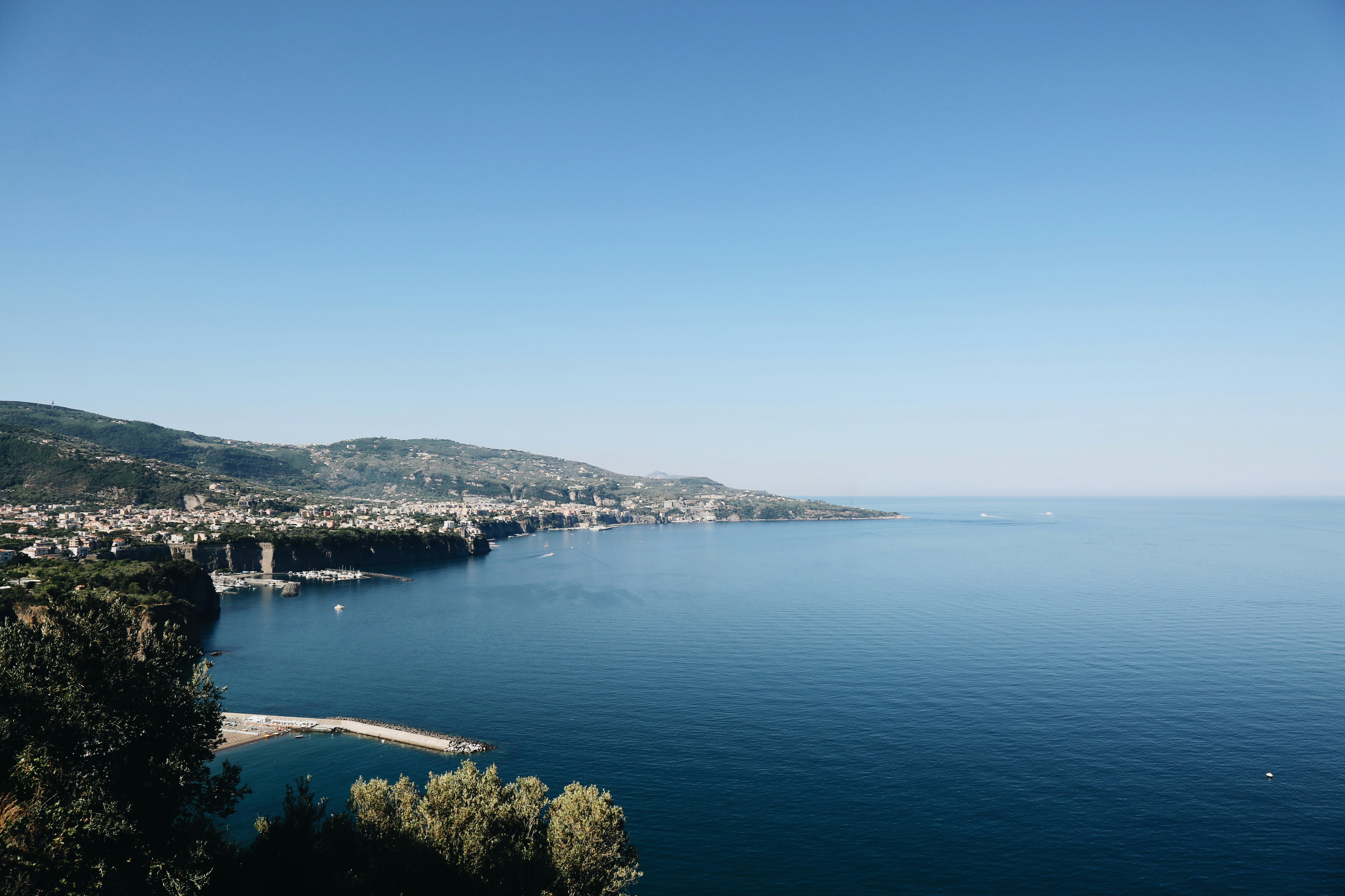 Expansive view of a serene coastline with distant mountains under a clear blue sky.