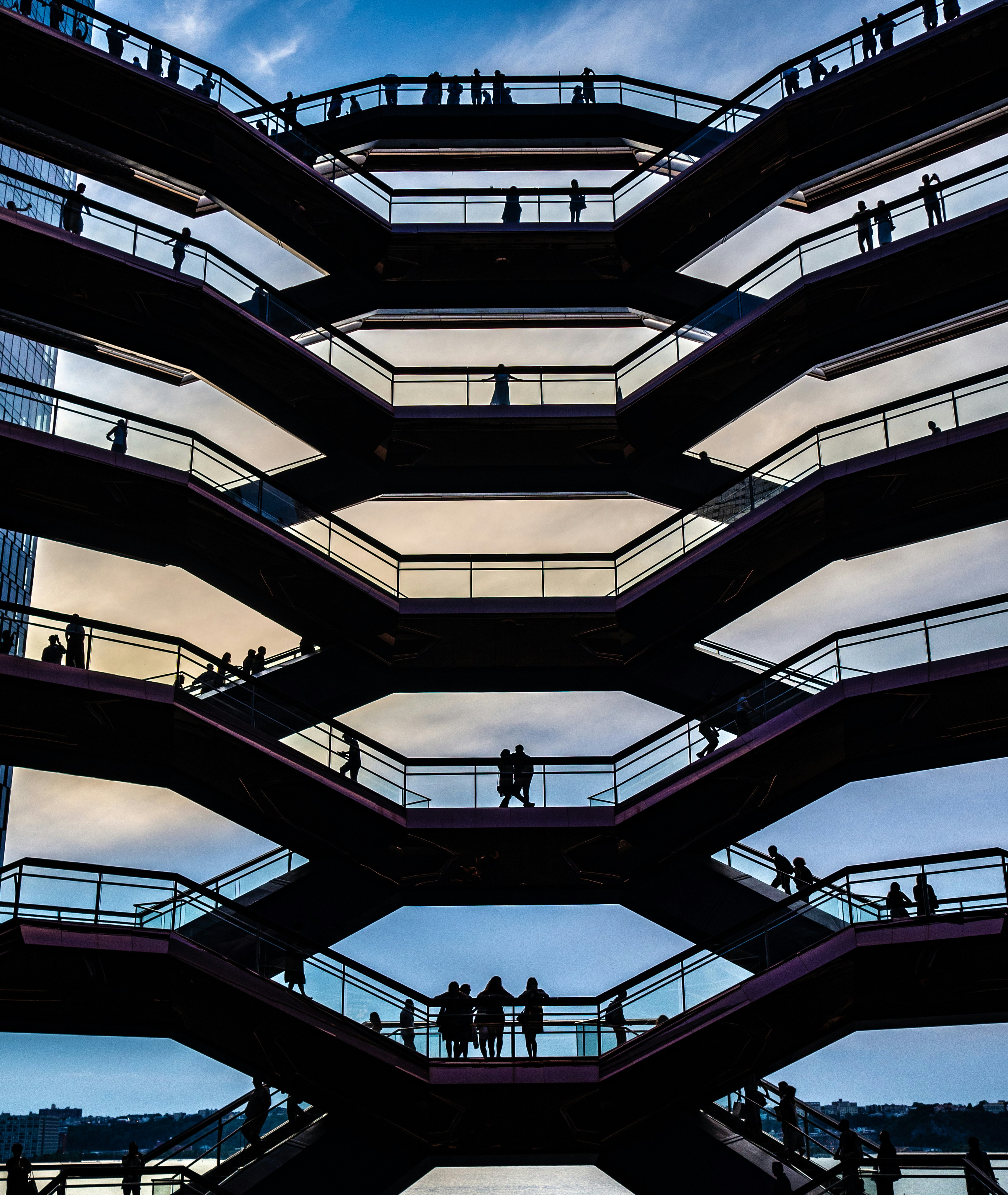 Silhouetted figures ascend a modern architectural marvel against a vibrant sky, showcasing the interplay of structure and movement.
