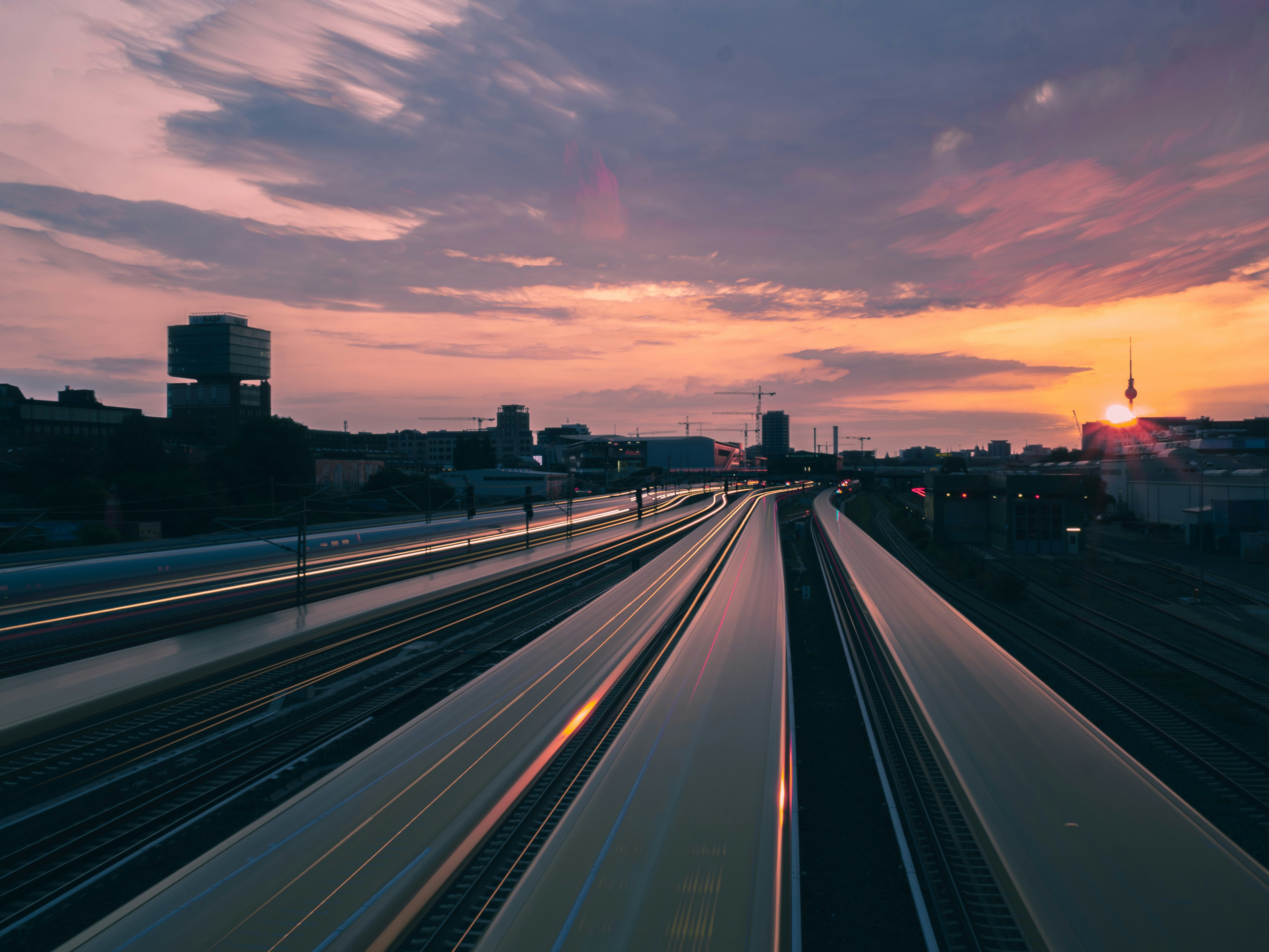 City skyline with blurred train tracks and a vibrant sunset casting warm hues.