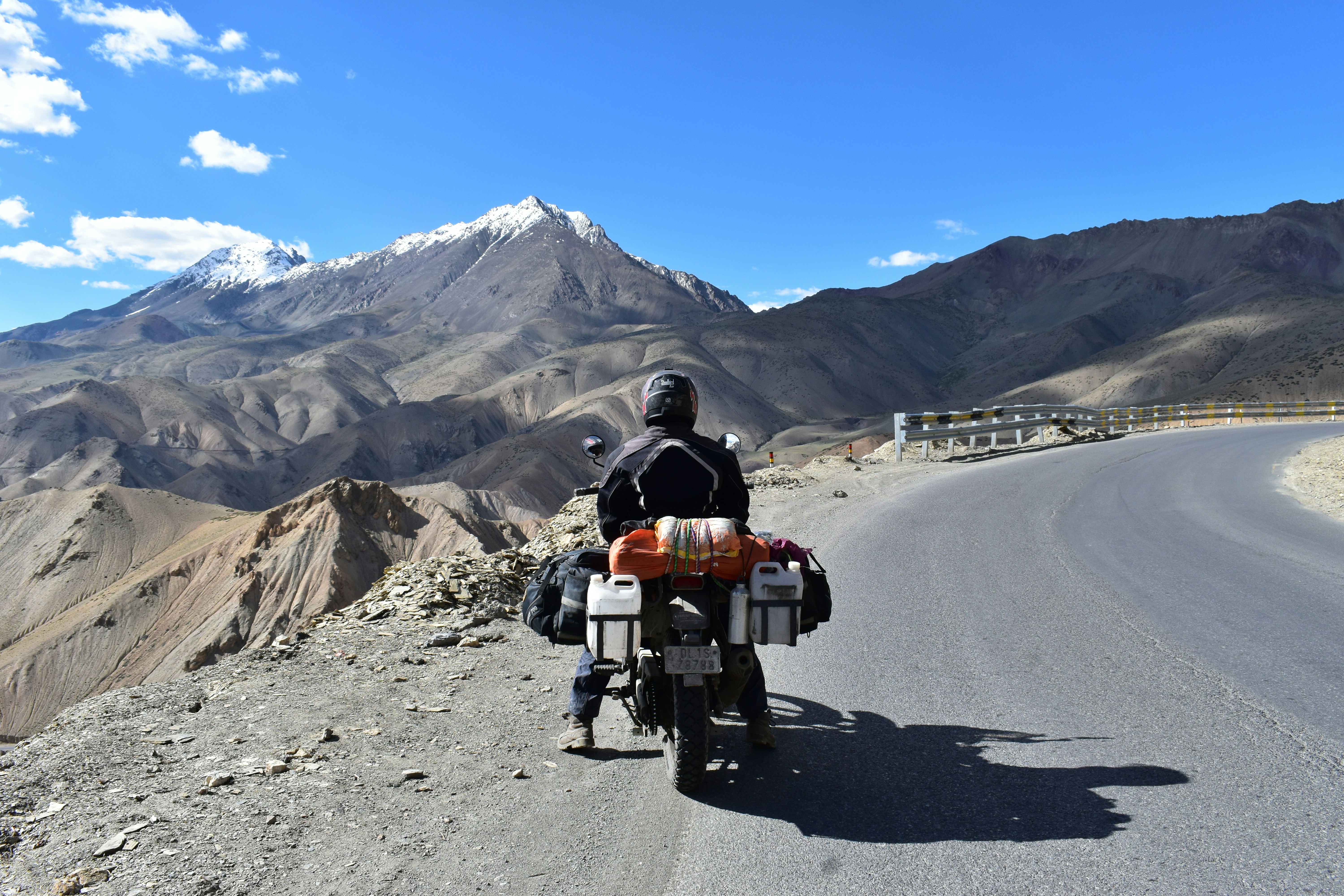 Motorcyclist navigating a winding road with snow-capped mountains in the background, showcasing the rugged beauty of the landscape.