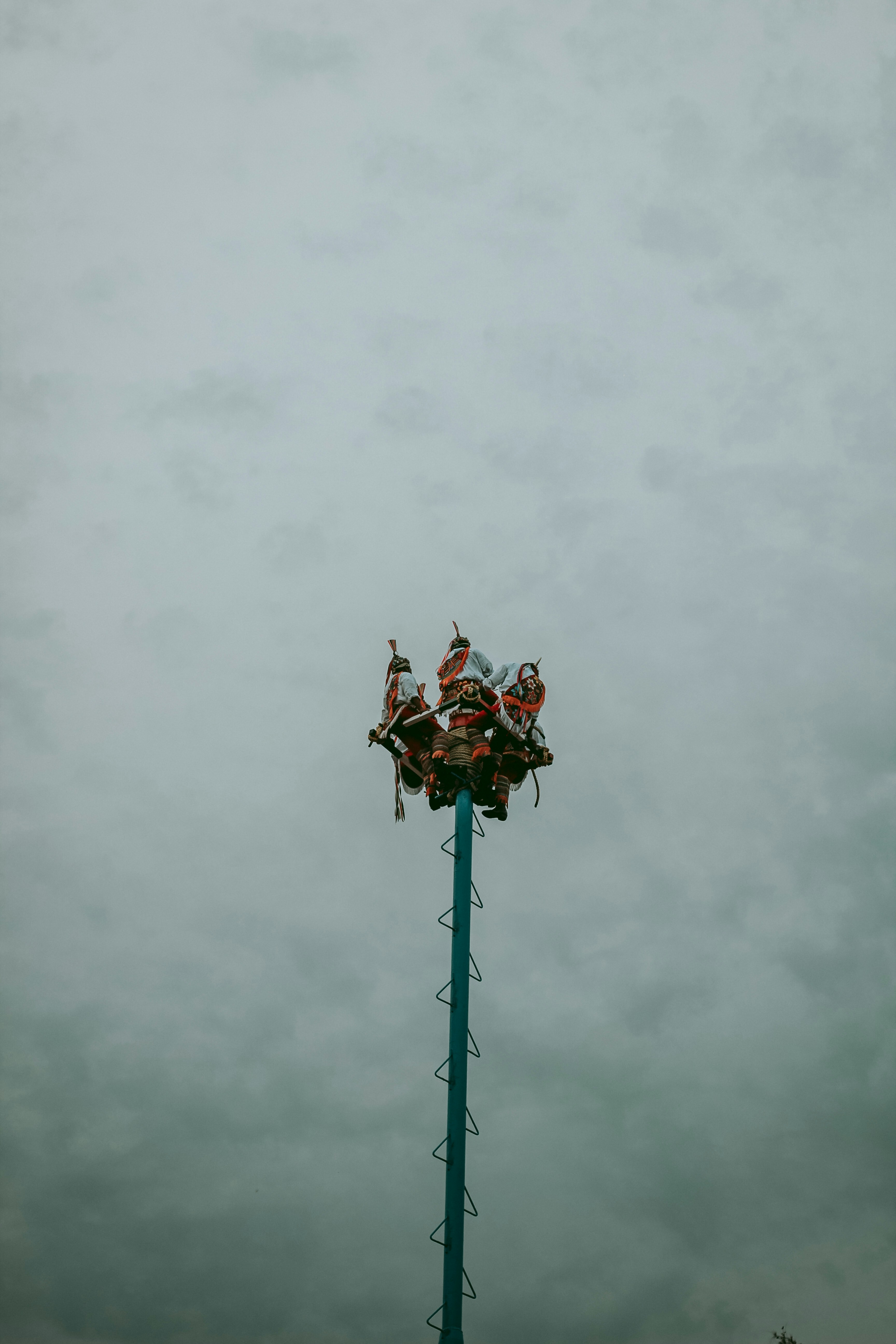 Group of performers atop a tall pole, showcasing traditional acrobatics against a cloudy sky.