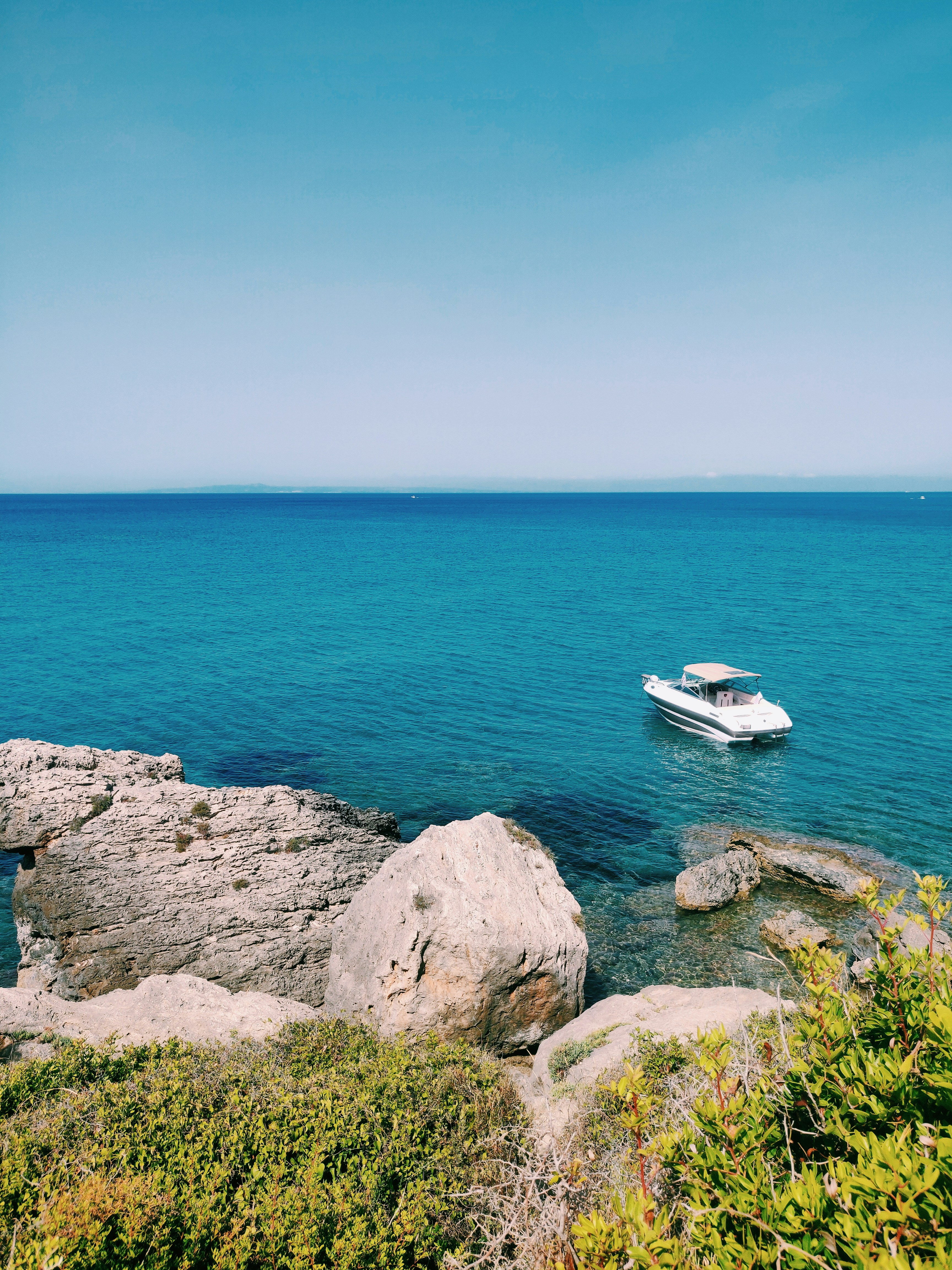 White yacht anchored near rocky coastline under clear blue sky.