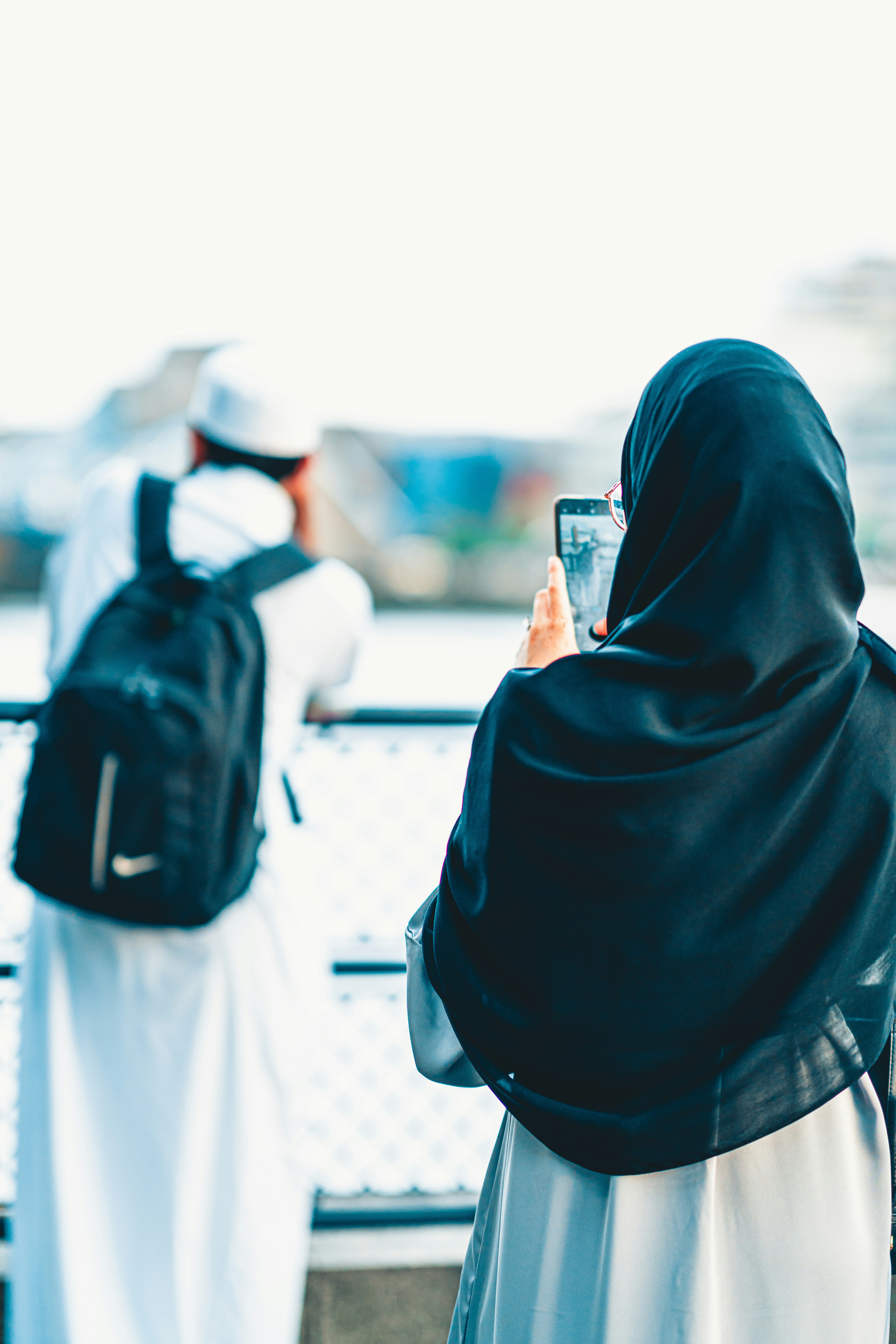 Woman in hijab headscarf taking photo of man leaning on chain link ...