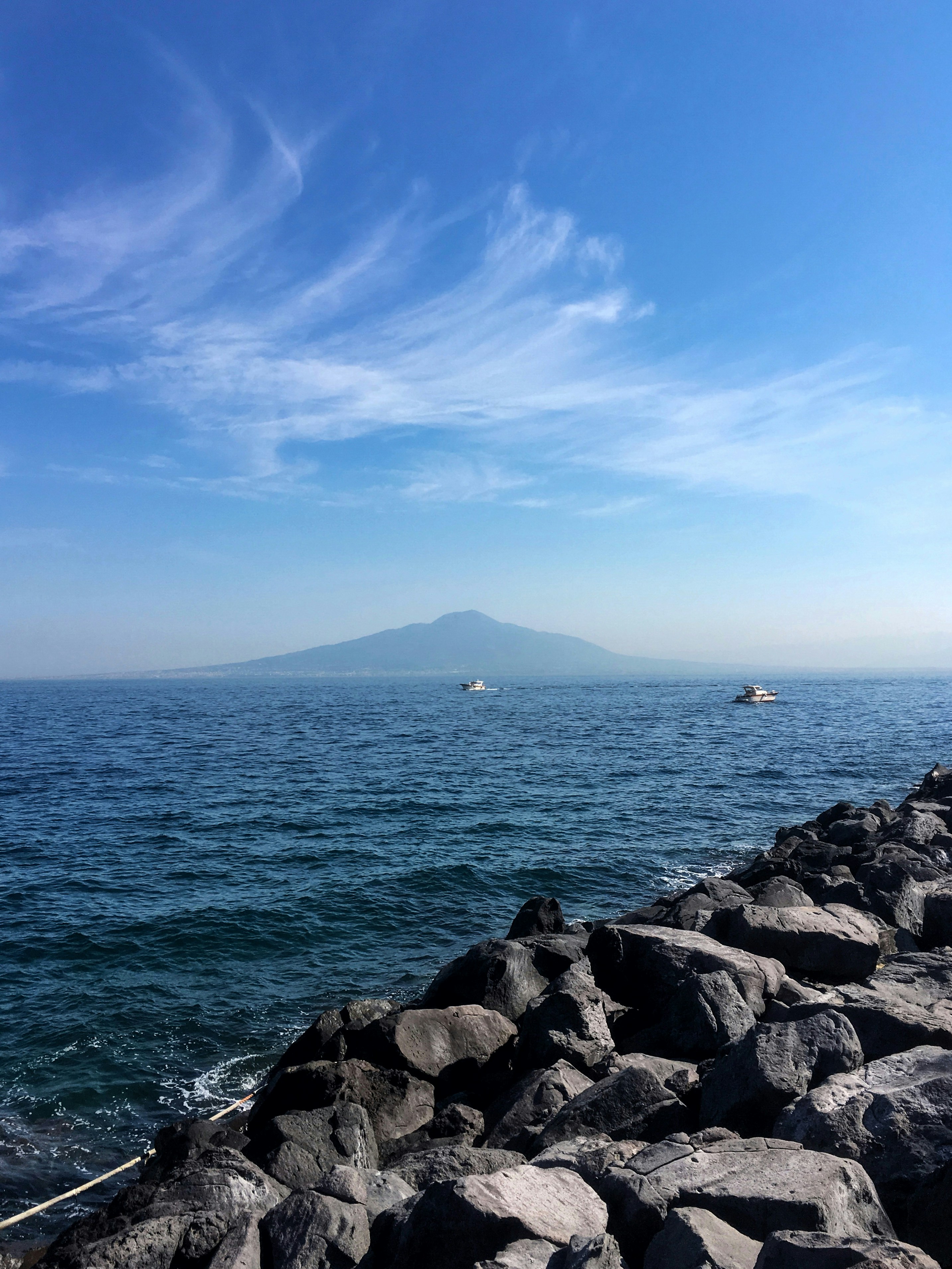 A serene coastal view featuring a distant volcanic island under a vibrant sky, with boats gently bobbing on the water's surface.