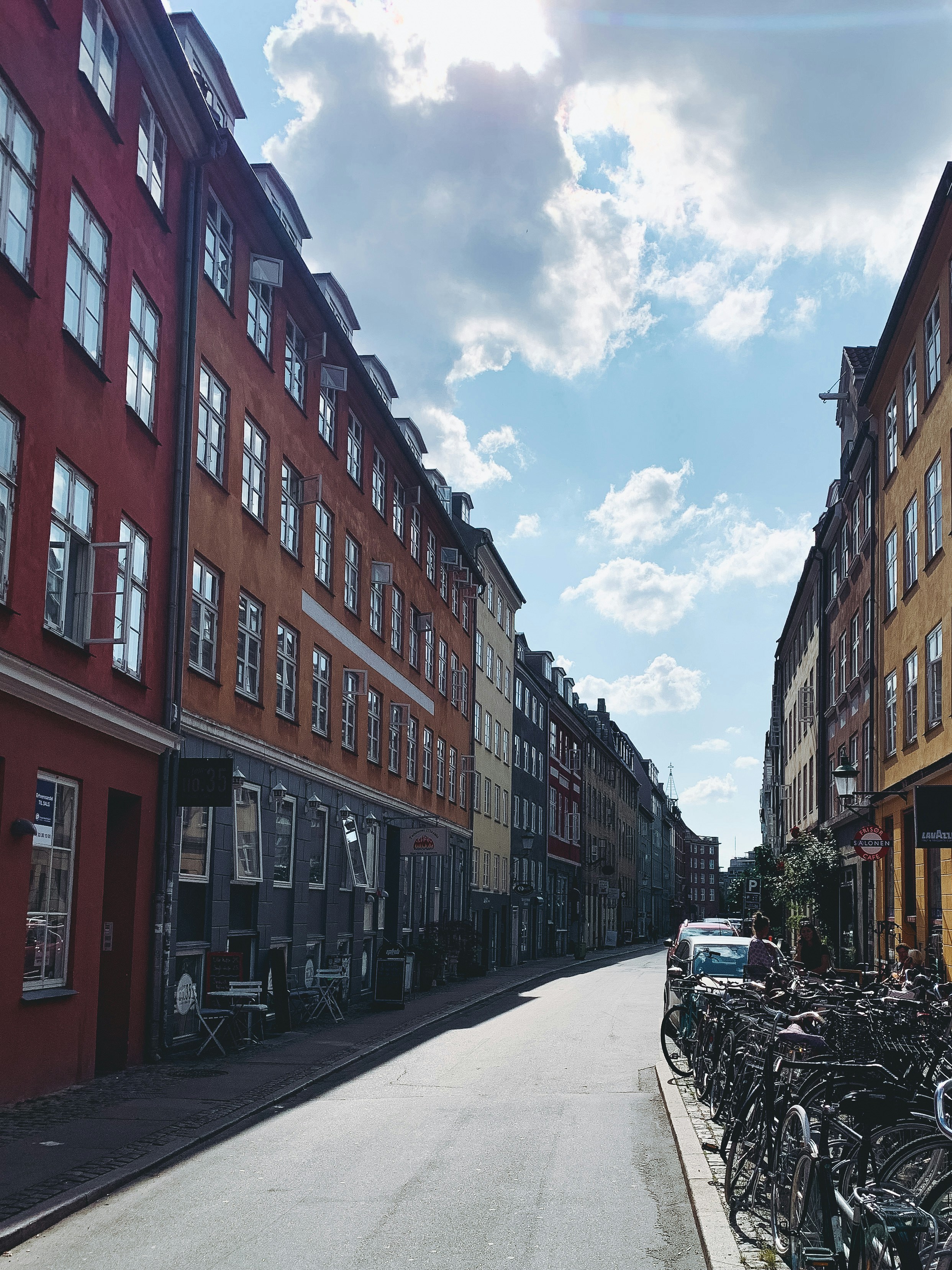 Colorful buildings line a quiet street in Copenhagen, with bicycles parked along the side and a clear blue sky above.