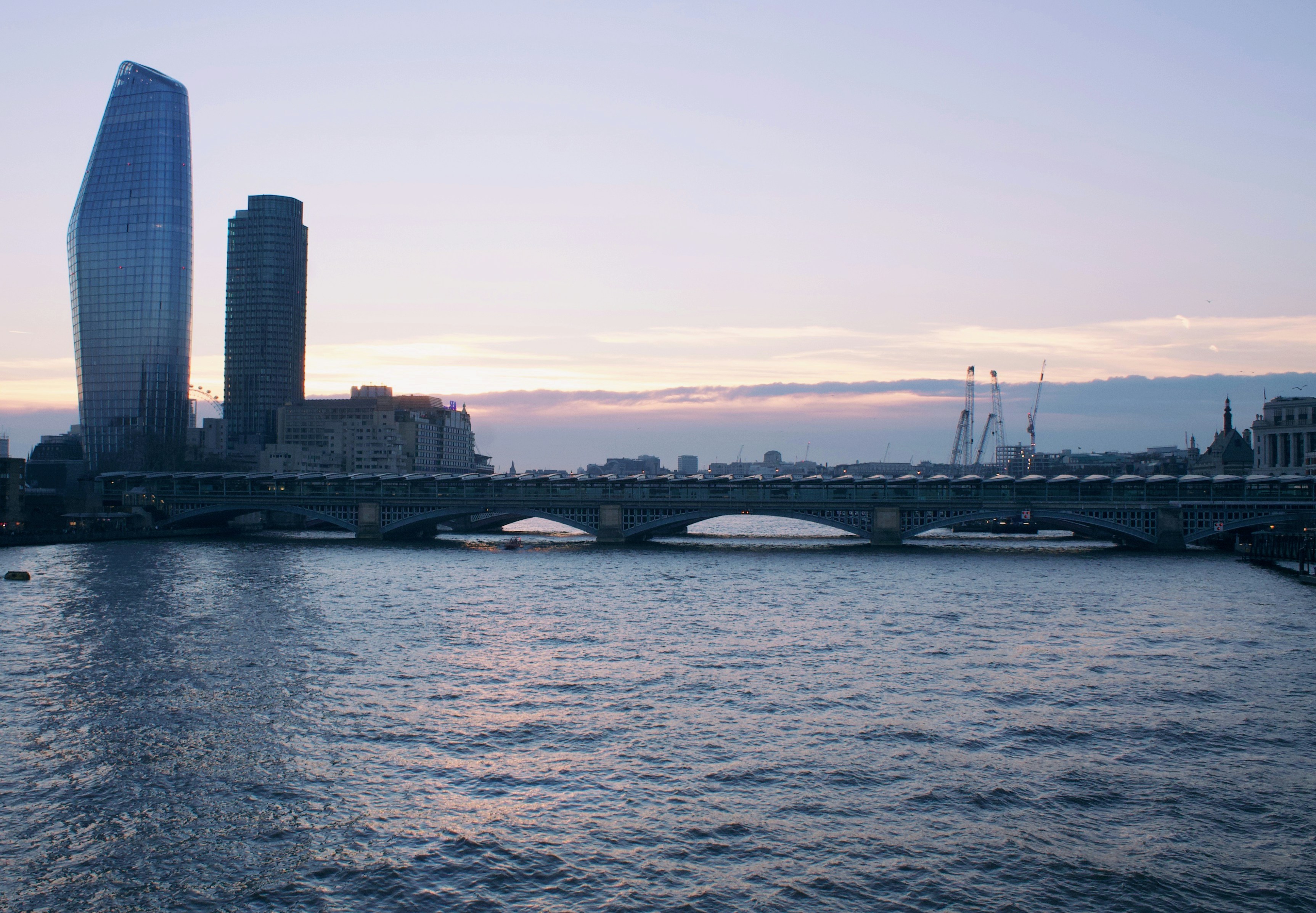 Silhouetted skyline with modern architecture against a twilight sky, reflecting on the water's surface.