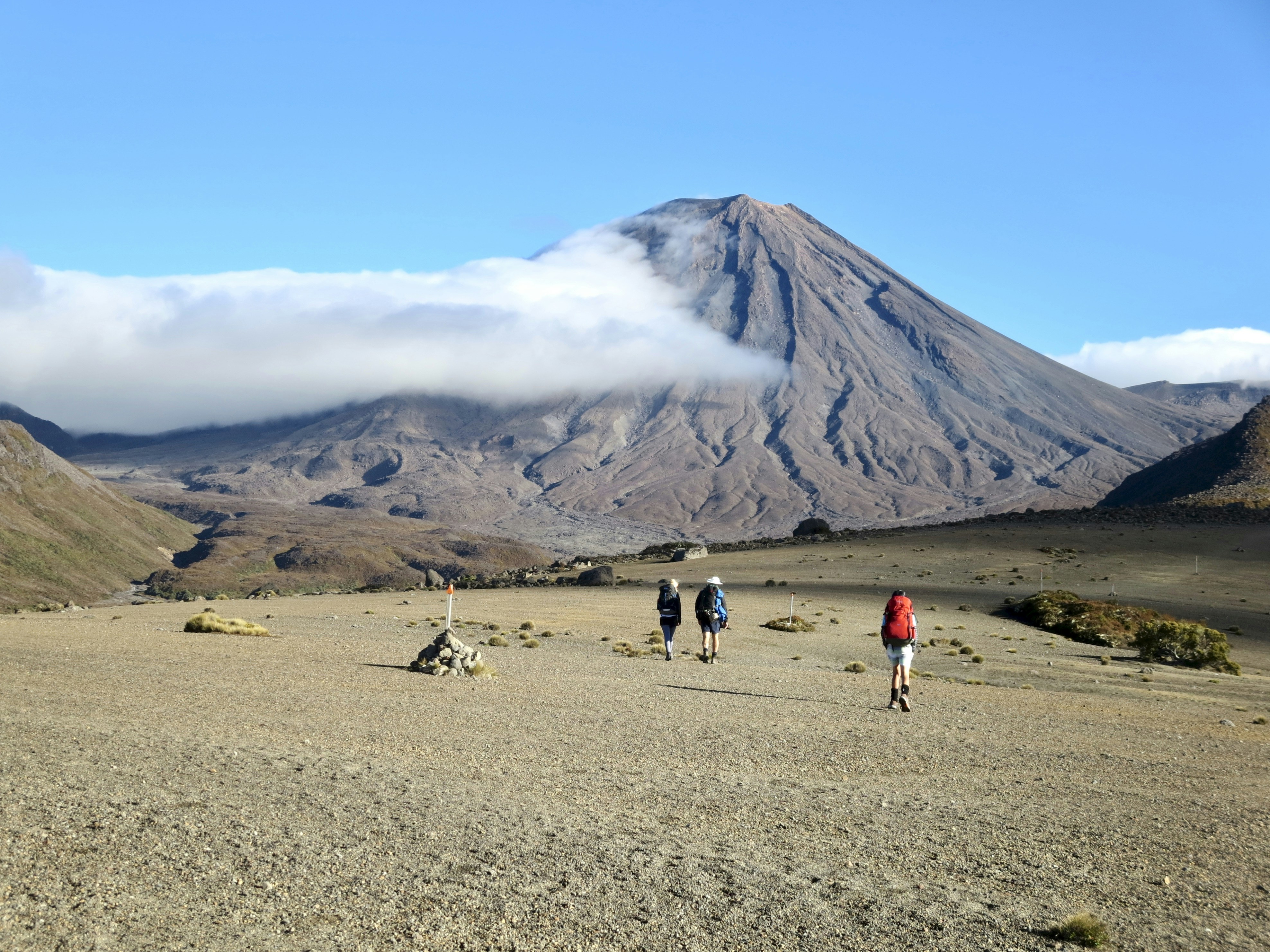 three people hiking going on mountain under blue and white skies