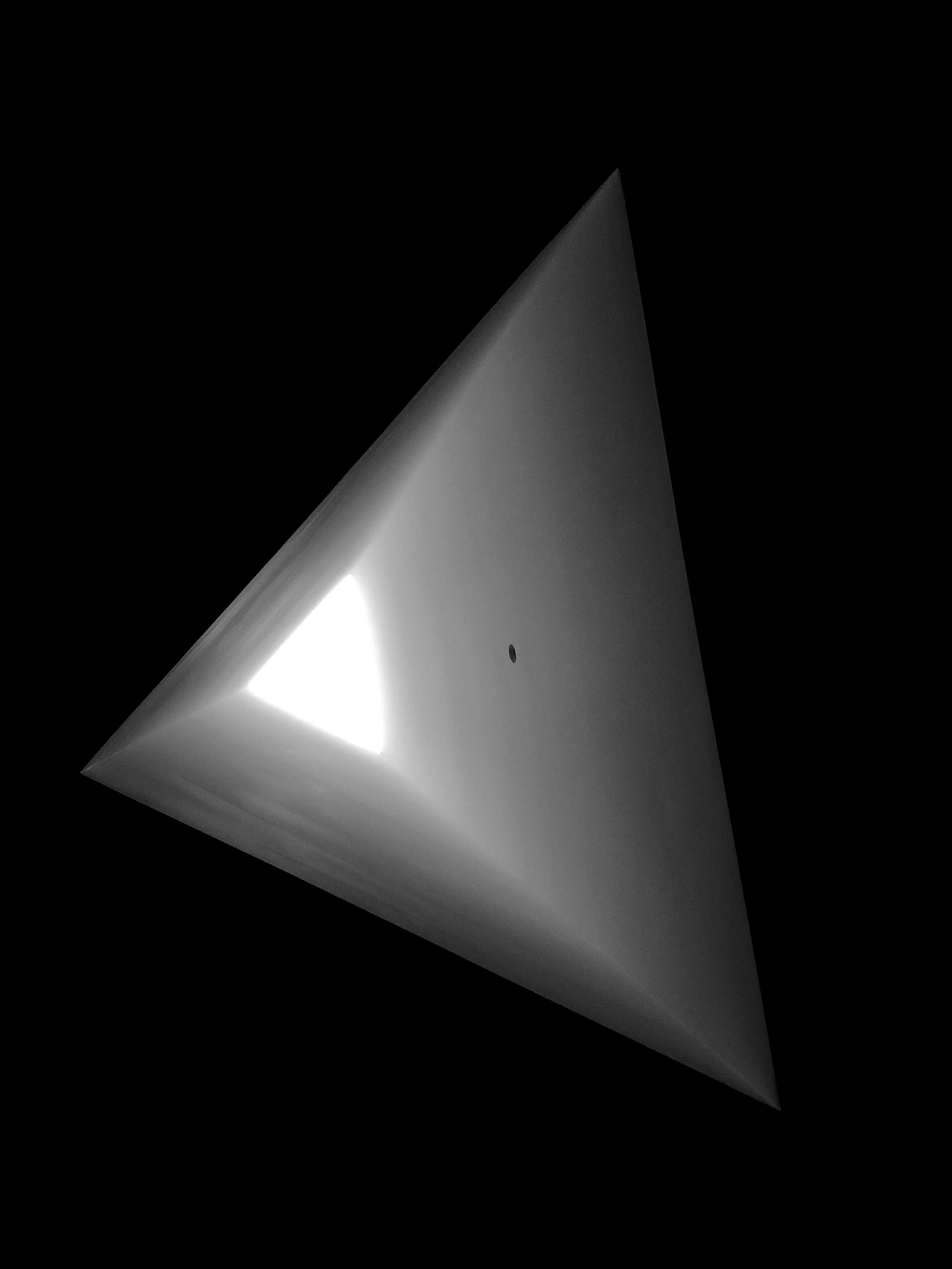 A triangular geometric form illuminated by a subtle light source, casting a shadow against a dark backdrop.