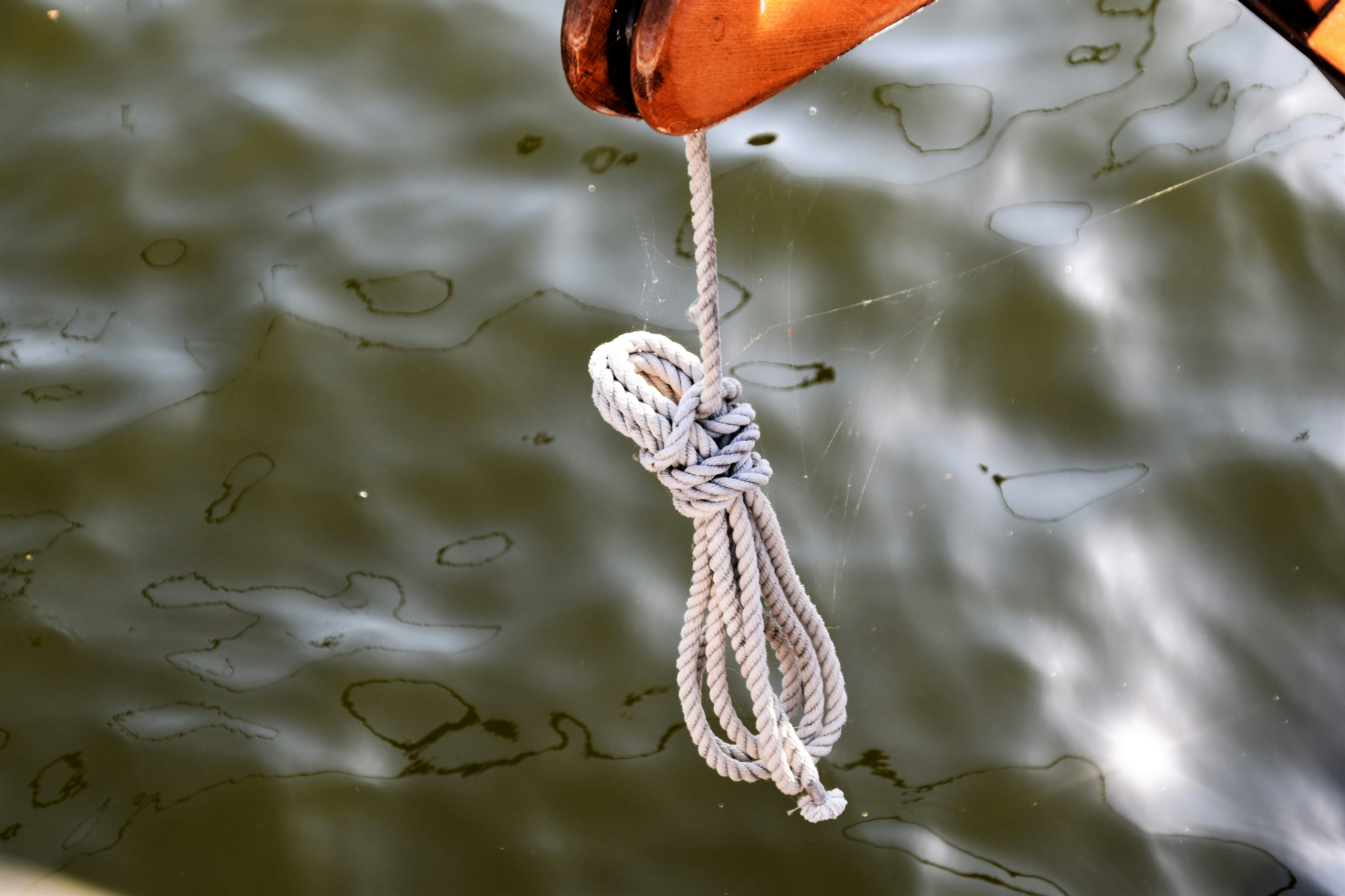 A neatly tied rope hangs above the reflective surface of water, capturing the interplay of light and shadow. The focus on the knot emphasizes craftsmanship and nautical themes.