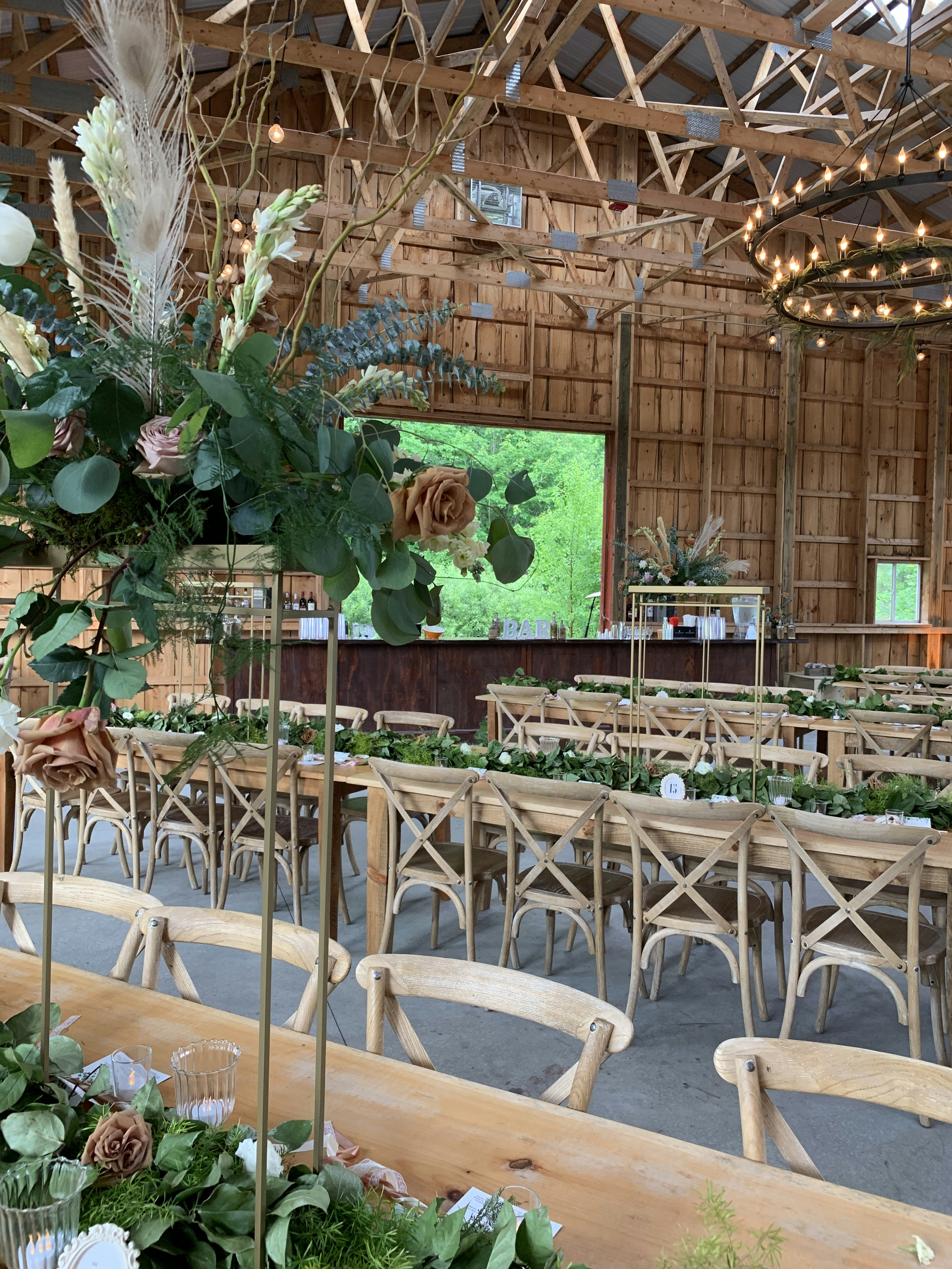 Elegant floral arrangements adorn wooden tables in a rustic barn setting, creating a warm atmosphere for an upcoming event.