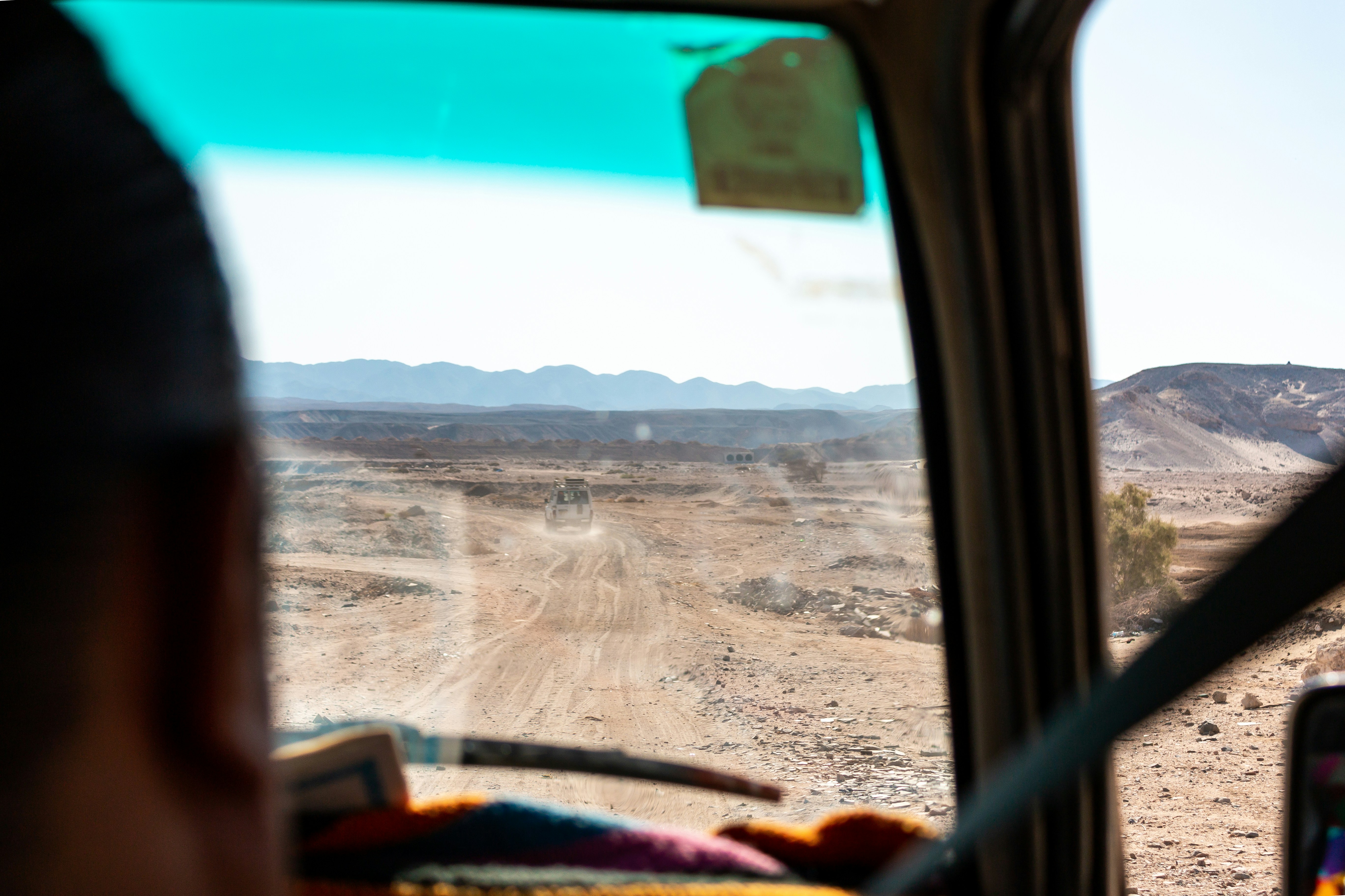 View of a barren desert landscape through a vehicle's windshield, with distant mountains under a clear sky.