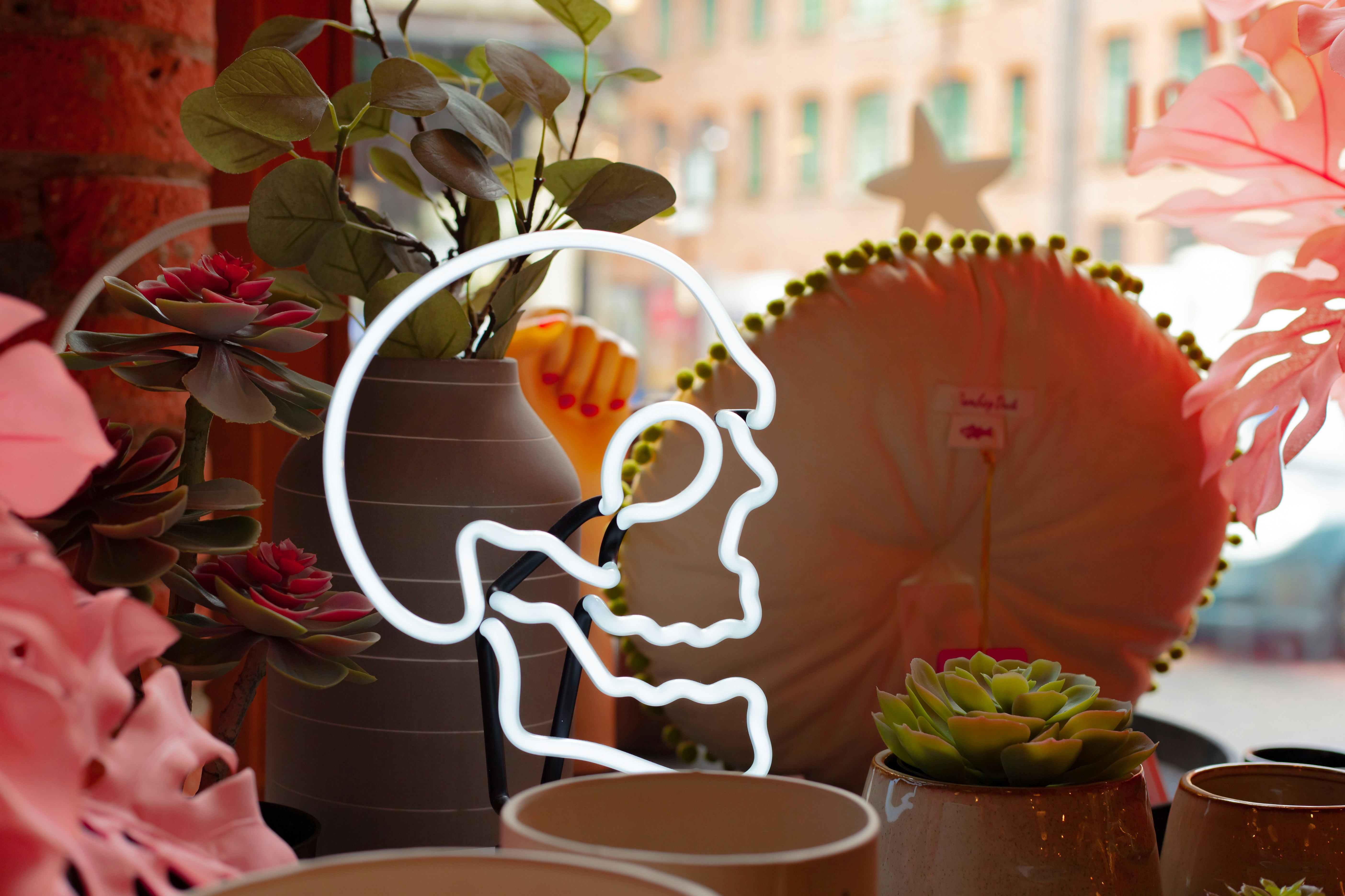 A neon skull outline juxtaposed with vibrant floral arrangements and decorative elements in a cozy storefront setting.