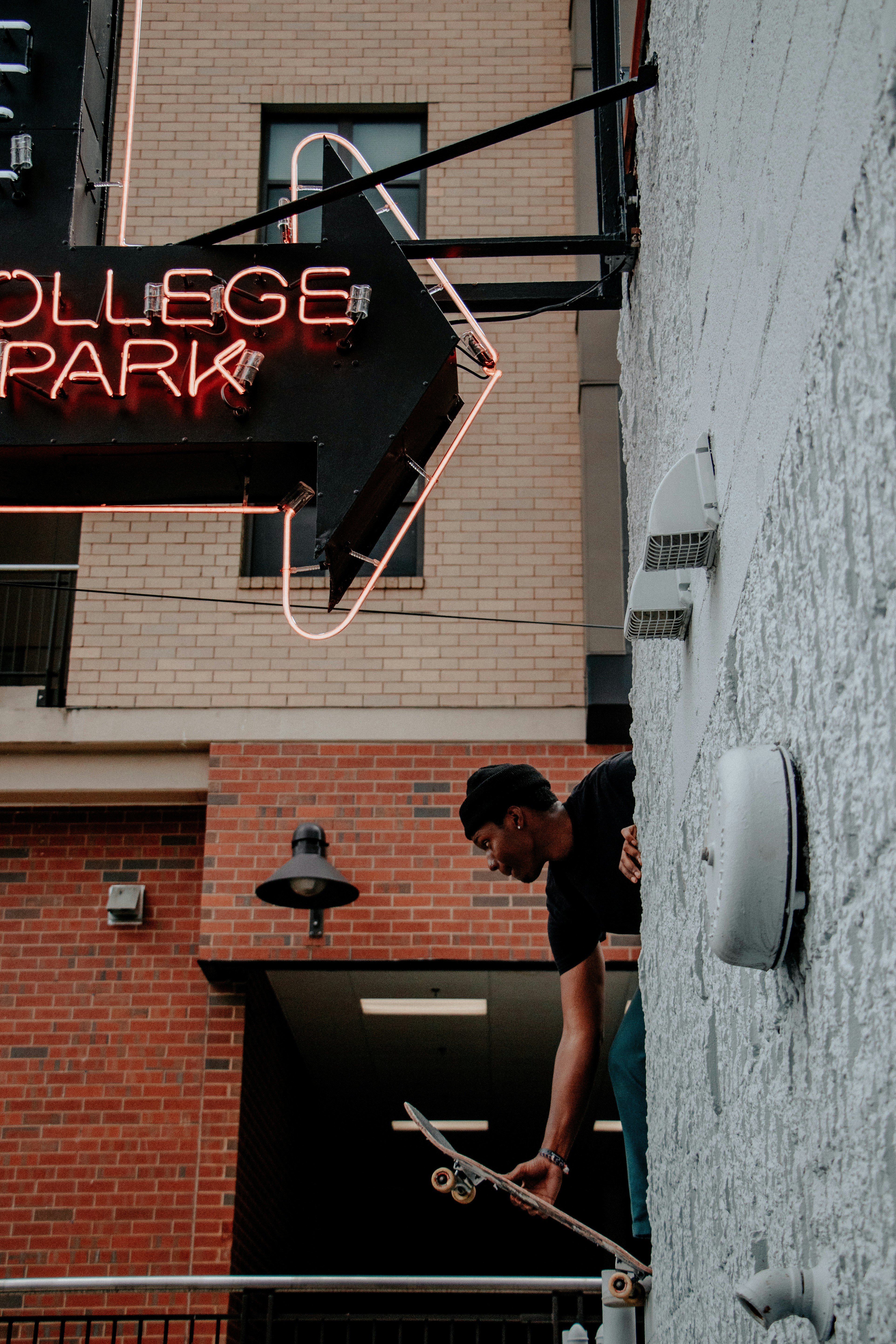 Skater poised to launch off a ledge with a neon 'College Park' sign illuminating the scene. The urban backdrop enhances the dynamic action.
