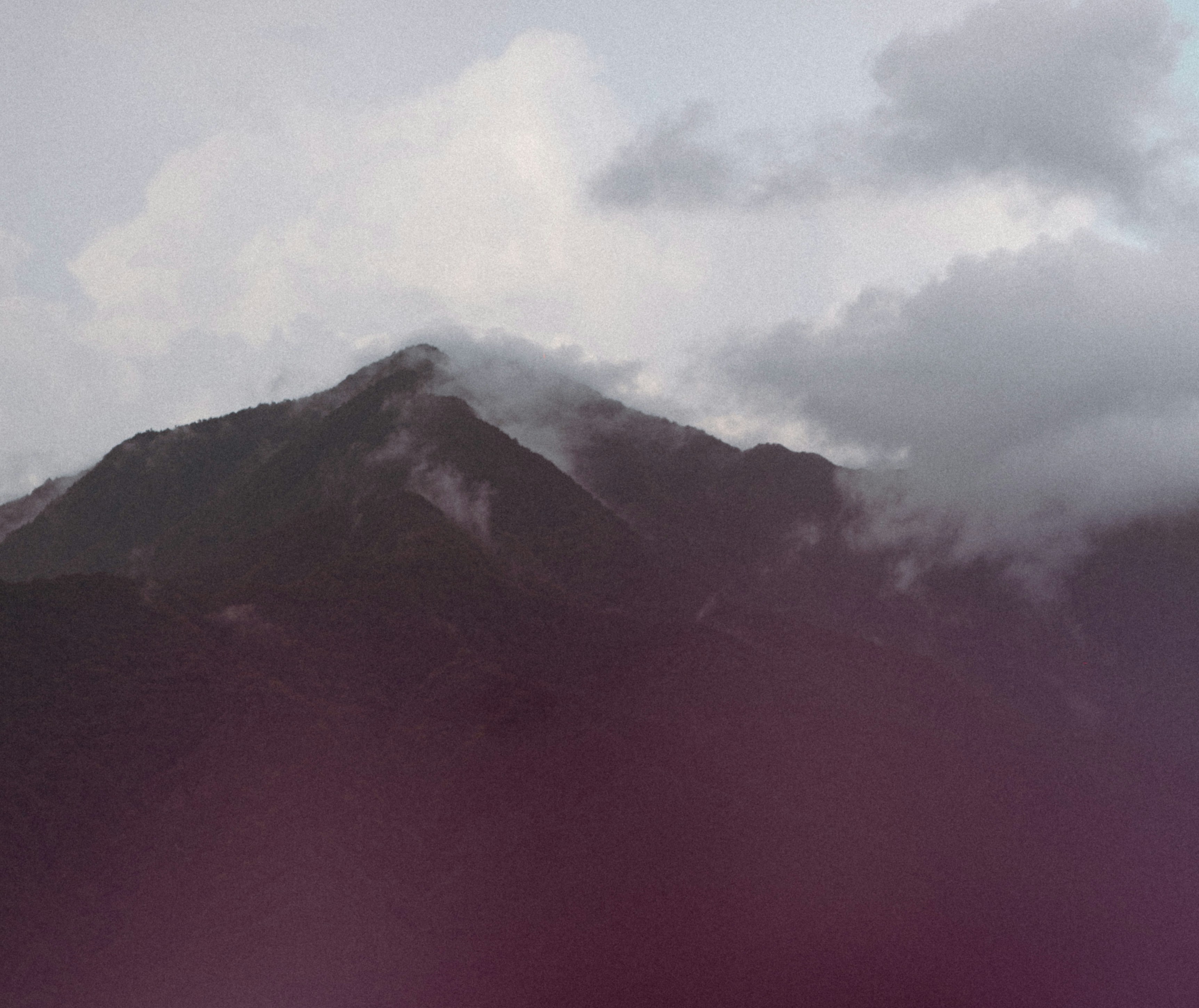 Cloud-shrouded mountain peaks with a hint of purple haze in the foreground.