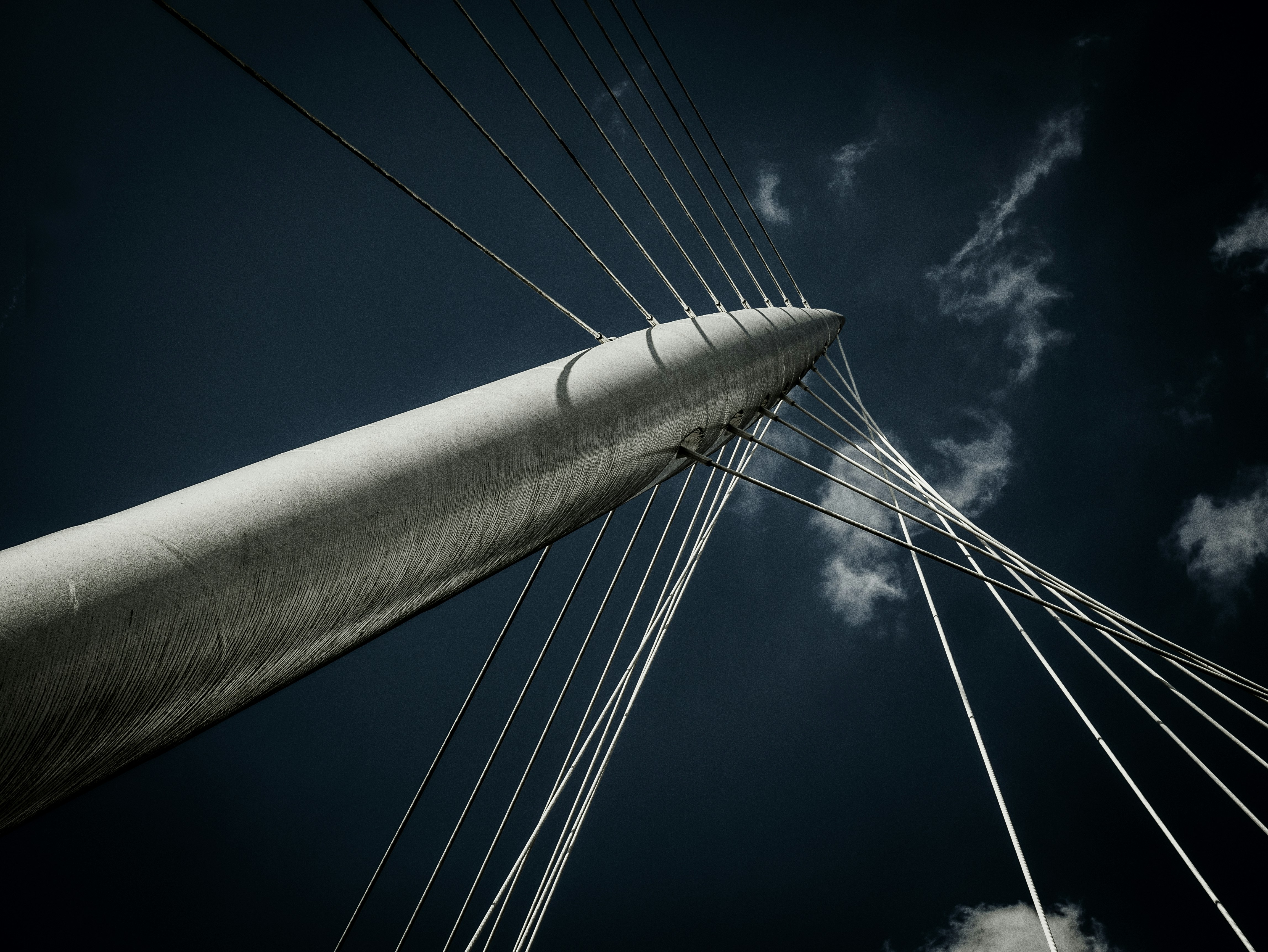A towering cable-stayed bridge pierces the sky, showcasing an intricate network of cables against a dramatic backdrop of clouds.