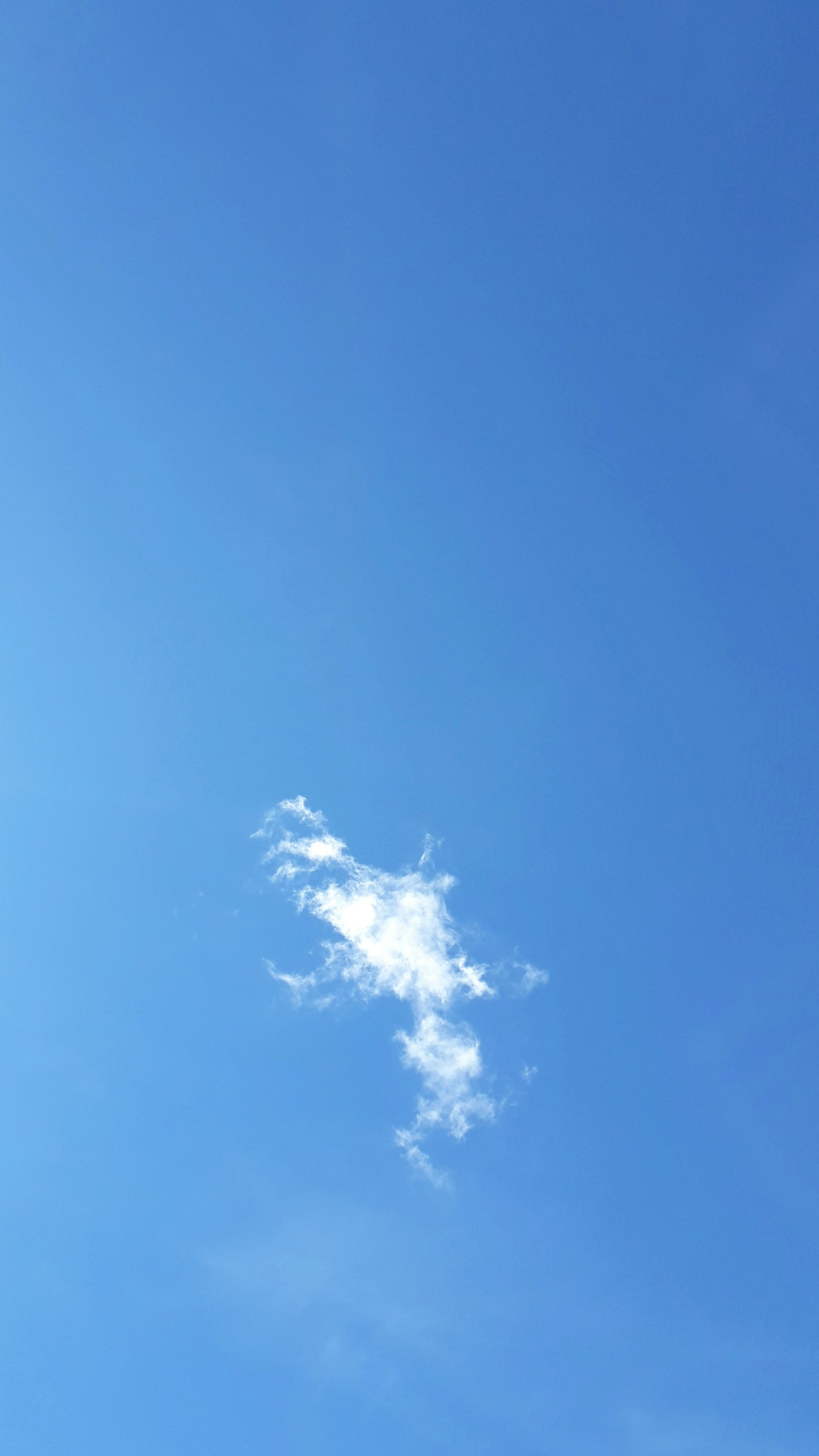 A solitary cloud drifting across a clear blue sky, embodying the tranquility of a sunny day.
