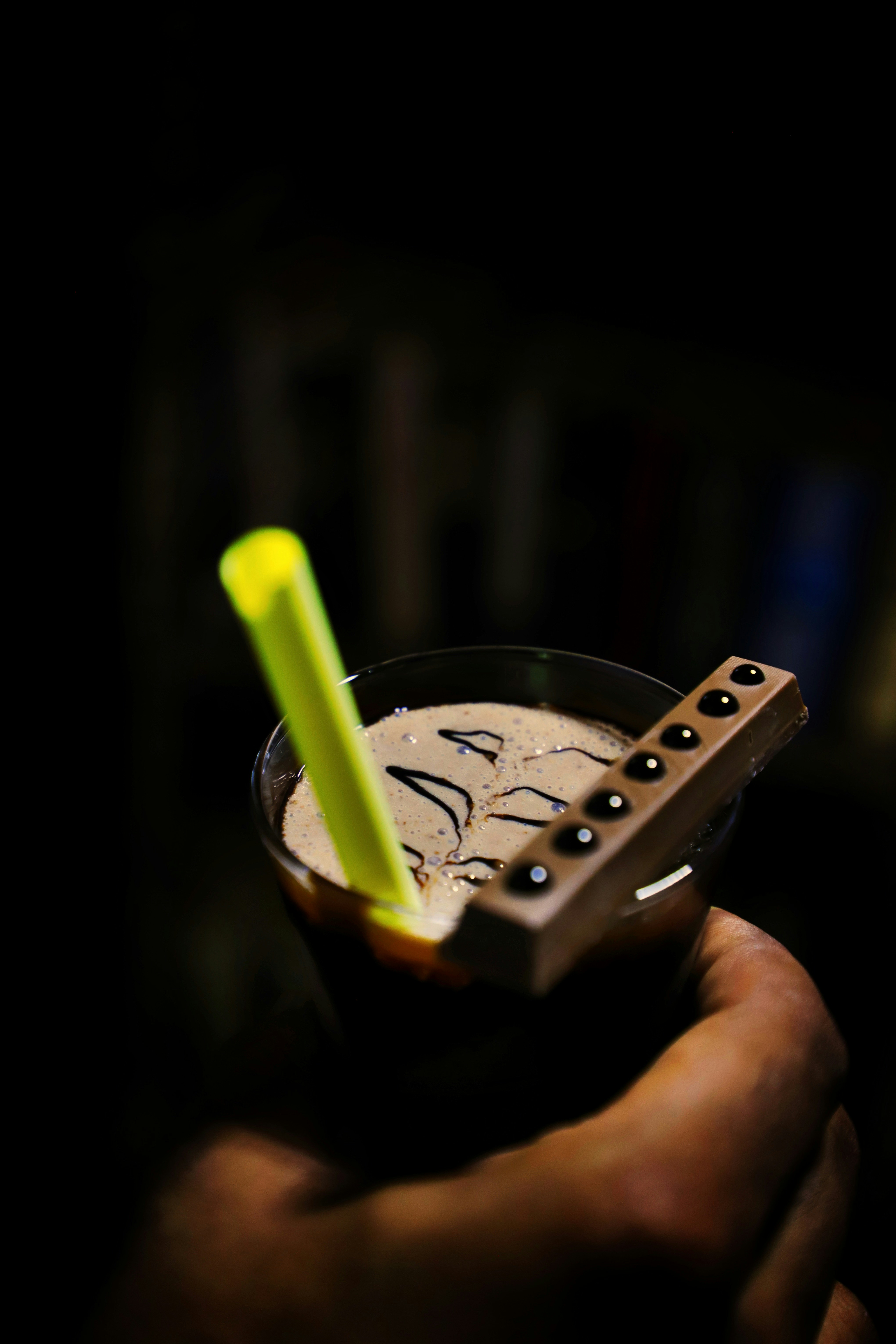 Neon-Stemmed Cocktail in Low Light, Crowned by a Chocolate Bar