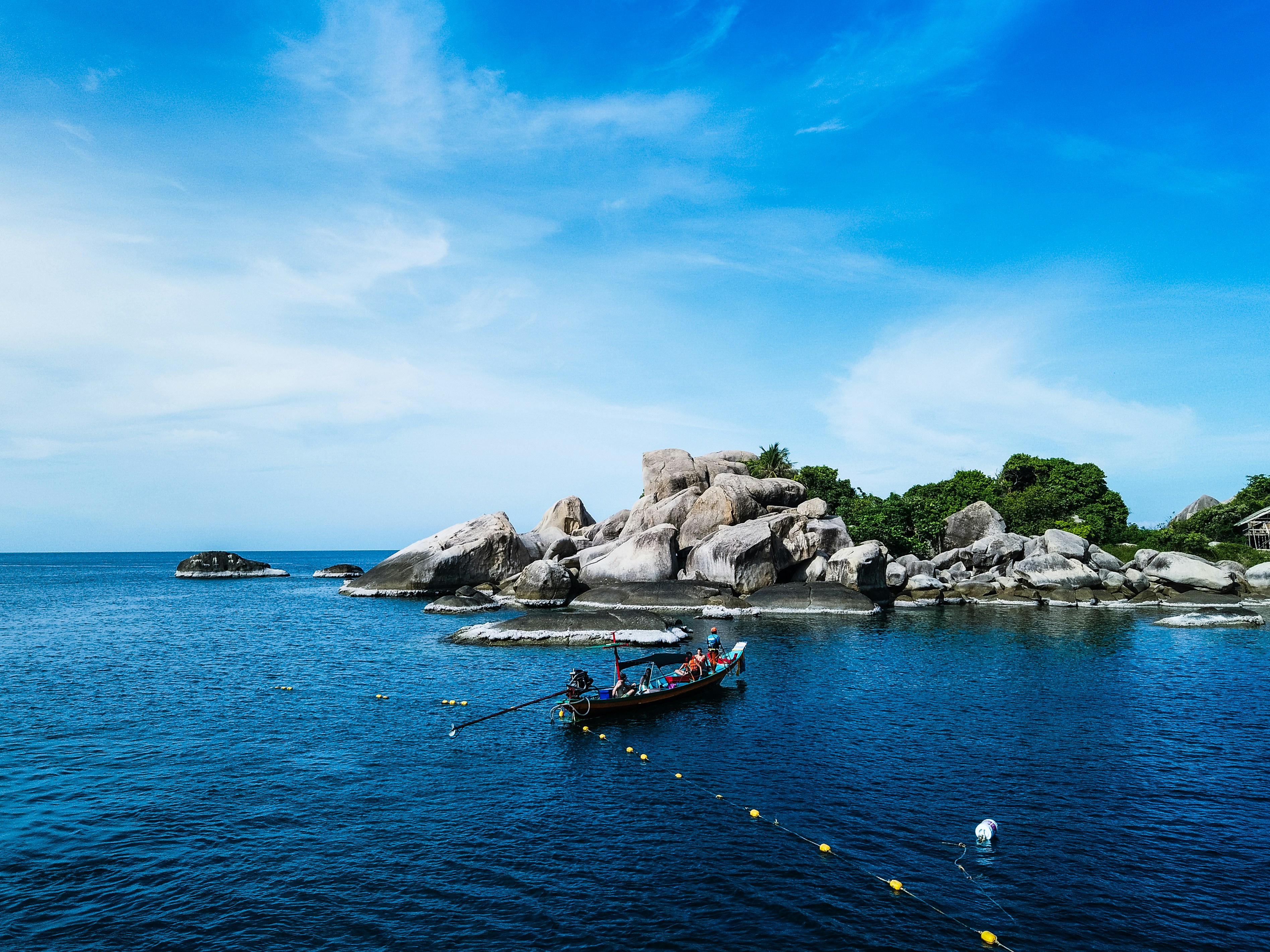 Small boat anchored near rocky island under a vibrant blue sky.