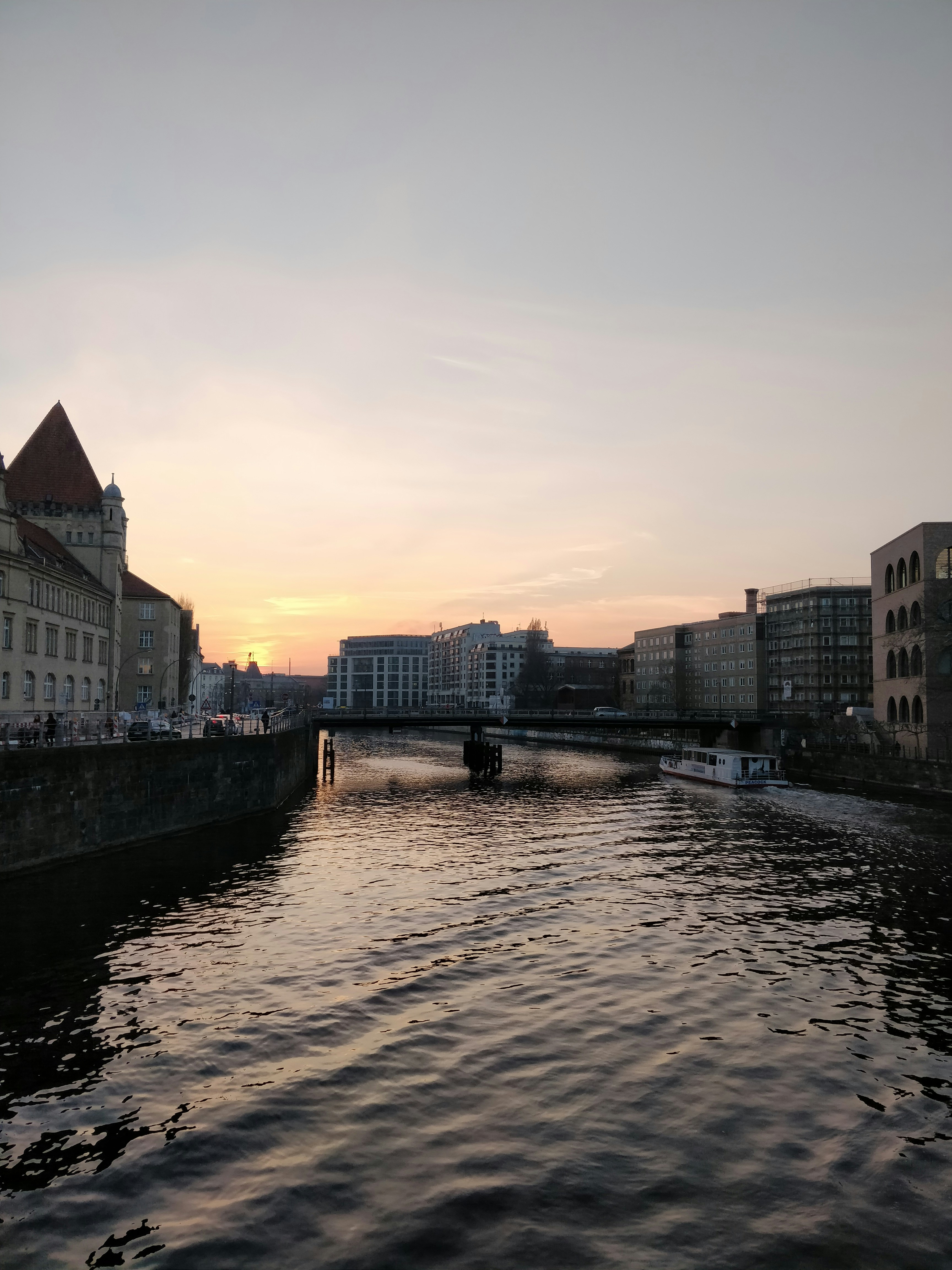 Cityscape with a canal reflecting the sunset, flanked by historic and modern buildings.