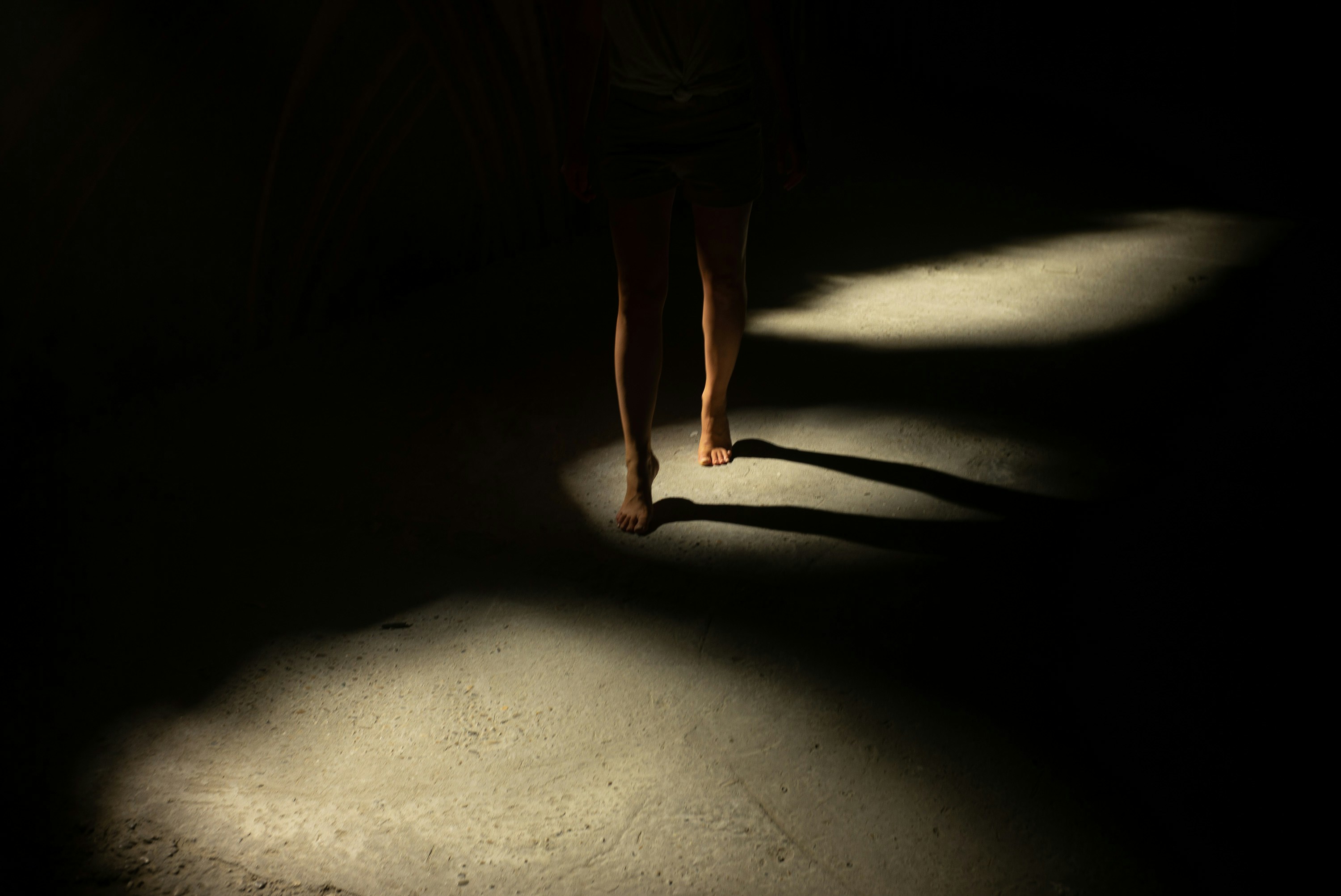 Bare feet walking through a dimly lit space with dramatic shadows on the floor.