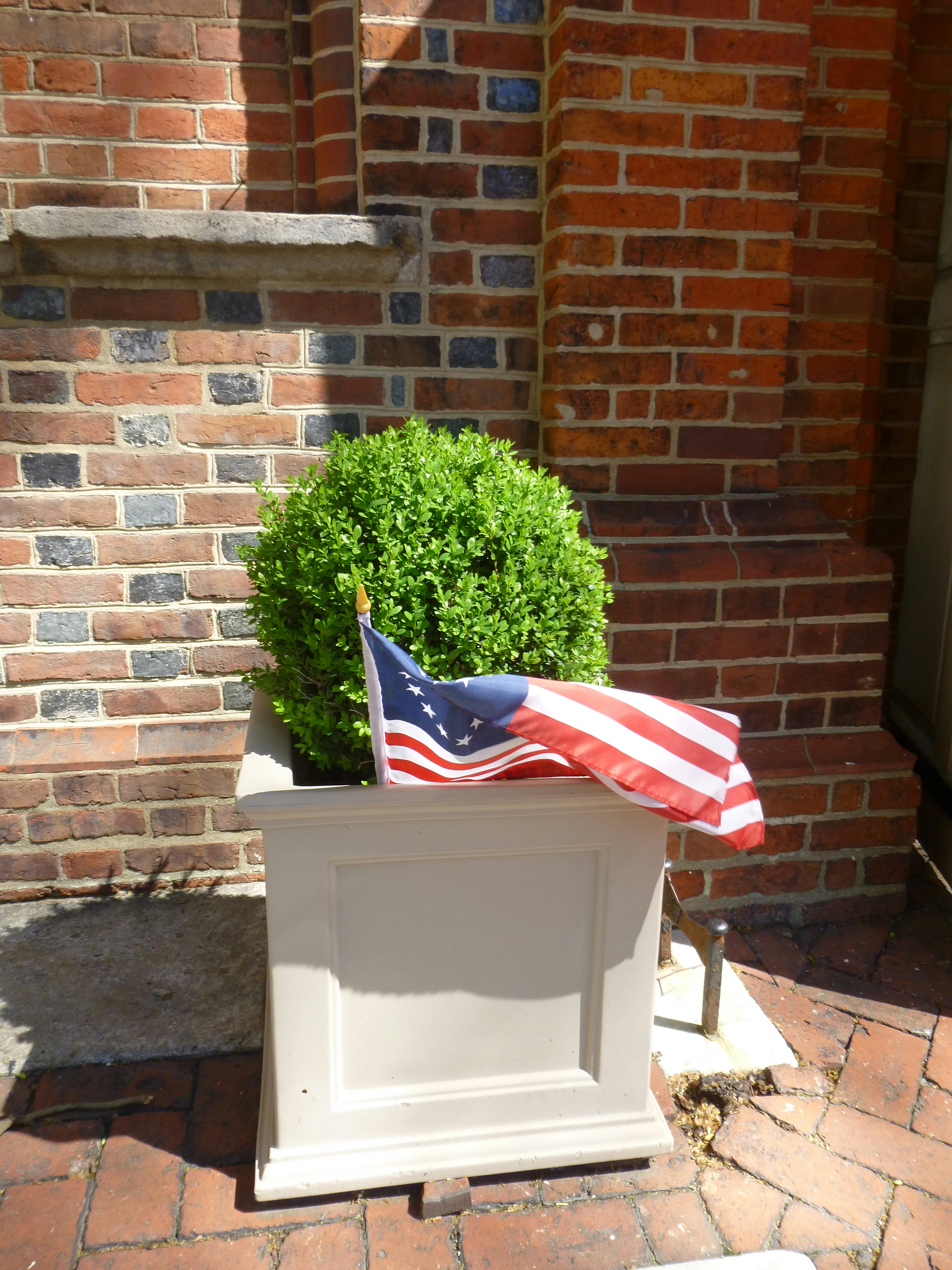 Flag Draped Over a Cream Planter Against a Red Brick Facade