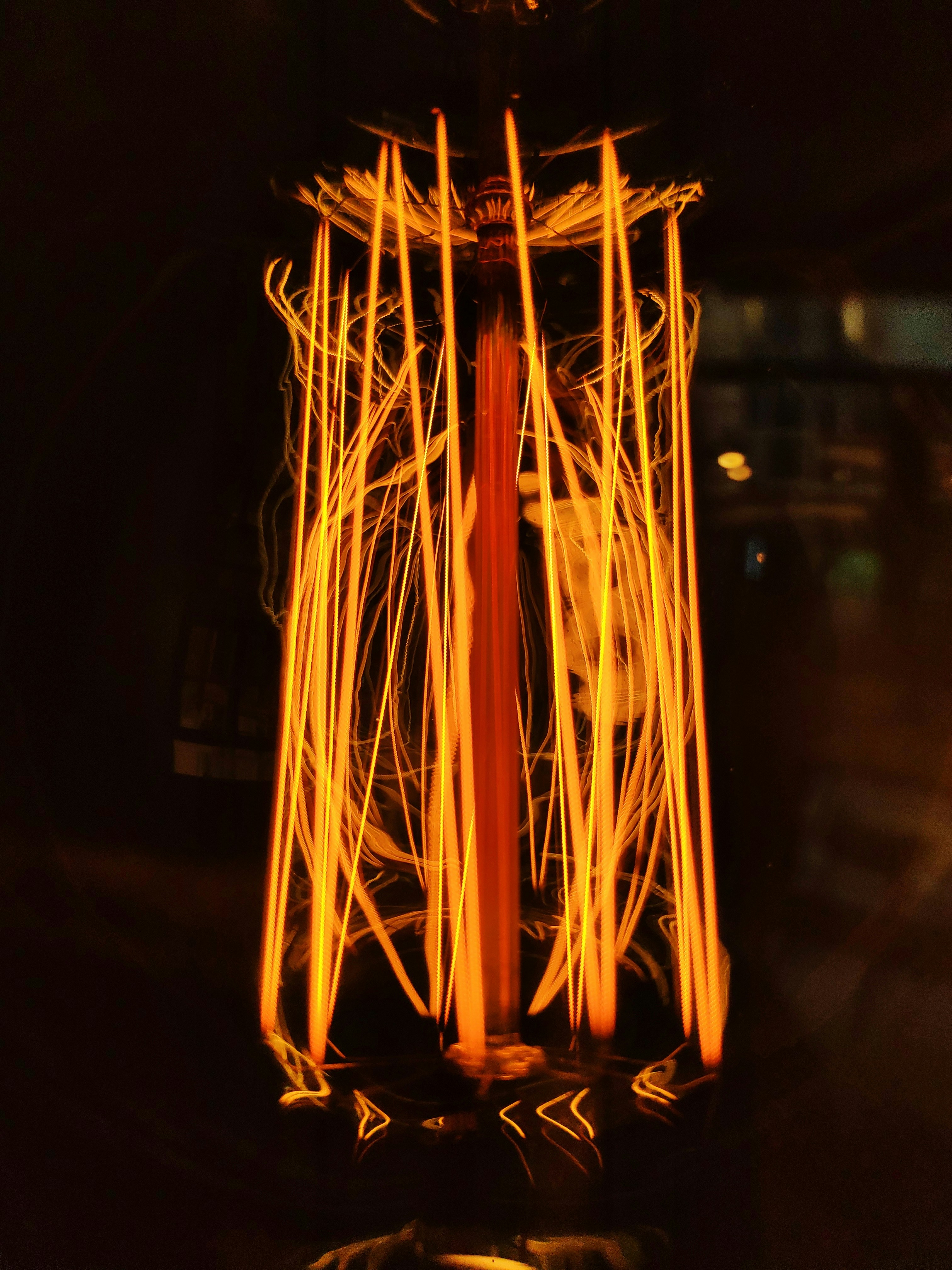 Photograph of a vintage Edison-style bulb with bright orange filaments forming vertical light trails around a dark central post.