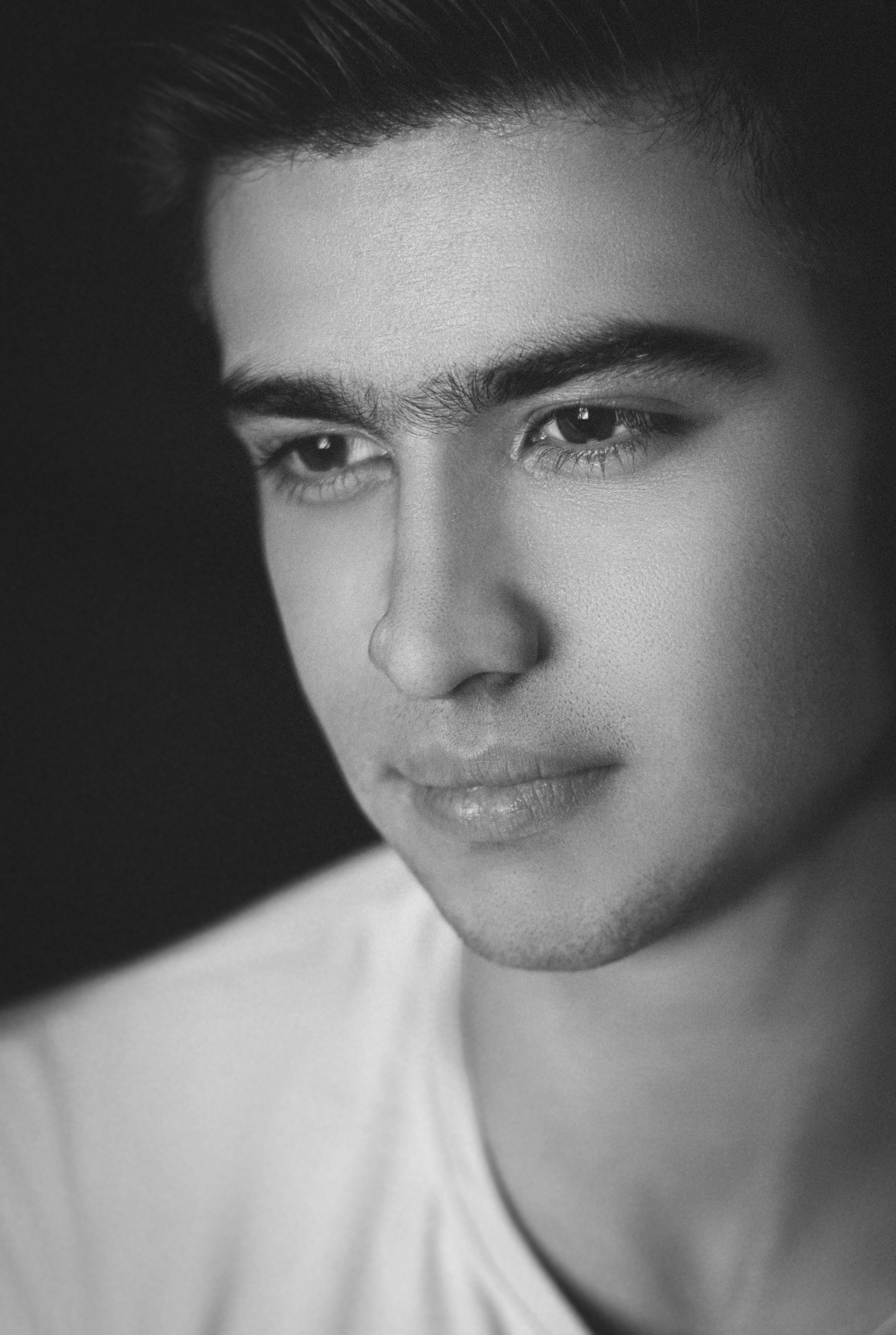 Close-up portrait highlighting a young man's contemplative expression in black and white. Soft lighting accentuates facial features.