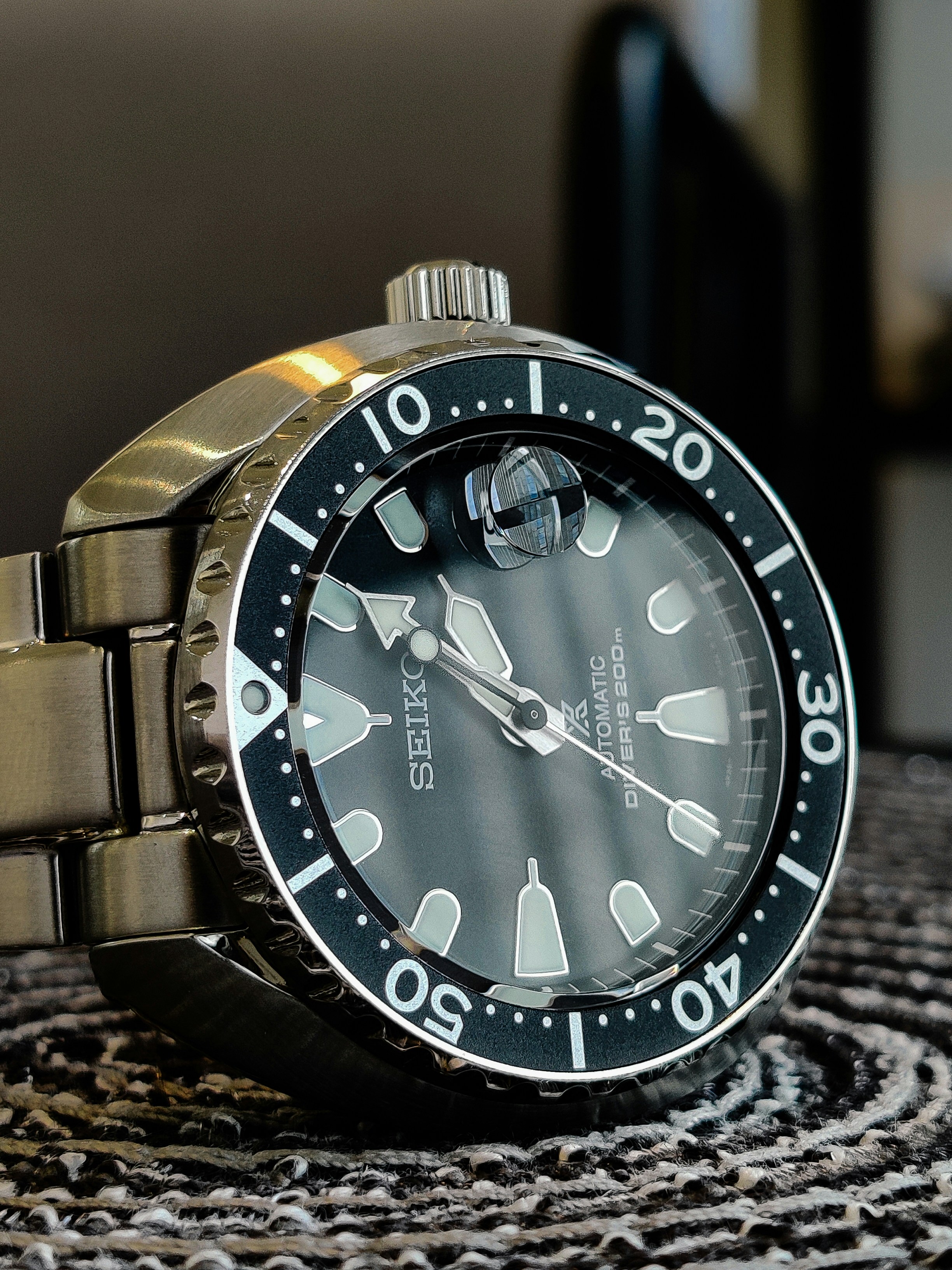 Close-up of a Seiko diver's watch on a textured surface, featuring a stainless steel bracelet, rotating bezel, and magnified date window.