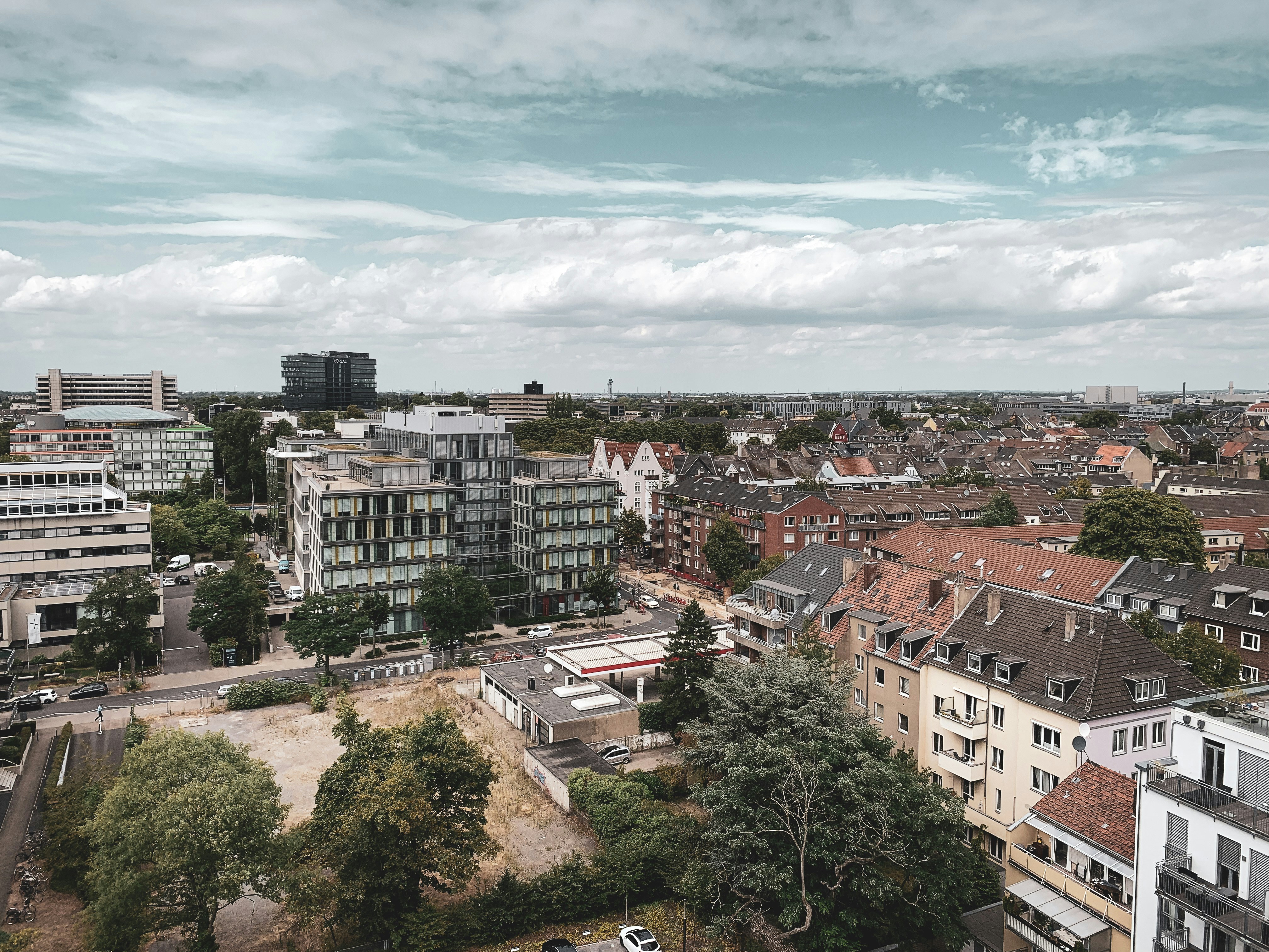 Aerial view showcasing a blend of modern architecture and traditional buildings in an urban landscape, with lush greenery interspersed throughout.