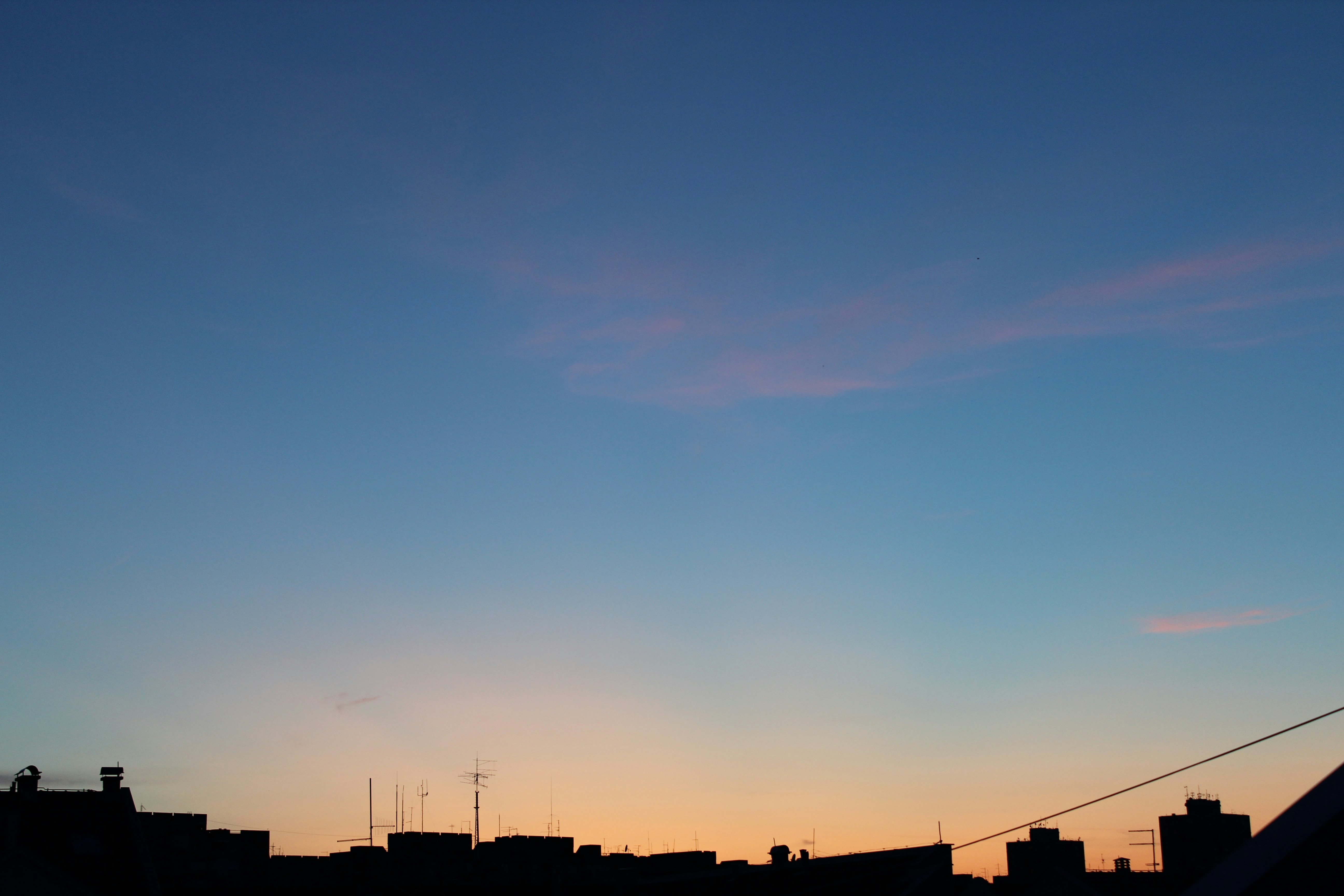 Silhouette of urban rooftops against a gradient twilight sky transitioning from blue to soft orange hues.