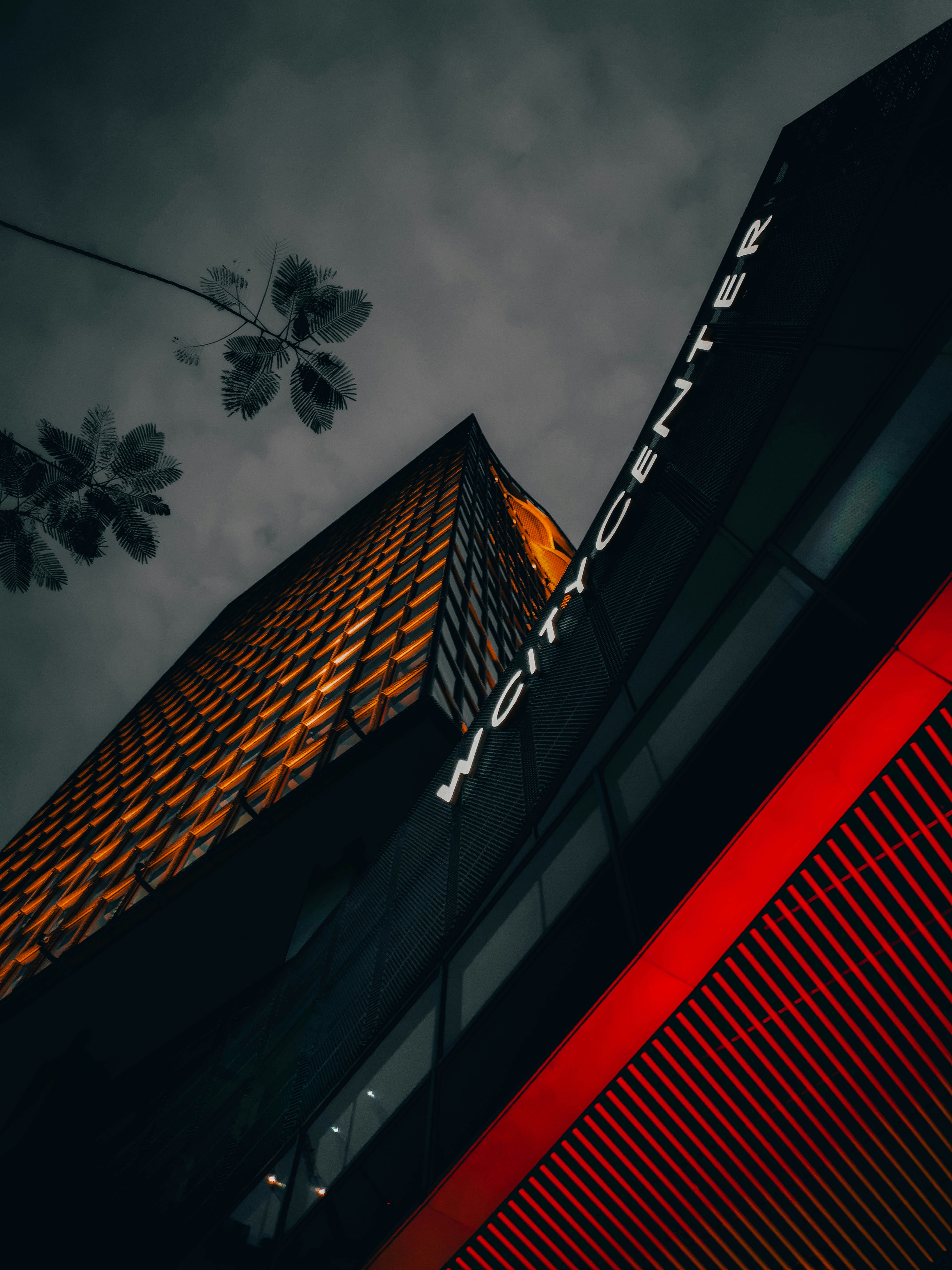 Diagonal urban tower bathed in warm orange light, rising across a moody sky. A low-angle shot emphasizes architectural texture and depth.