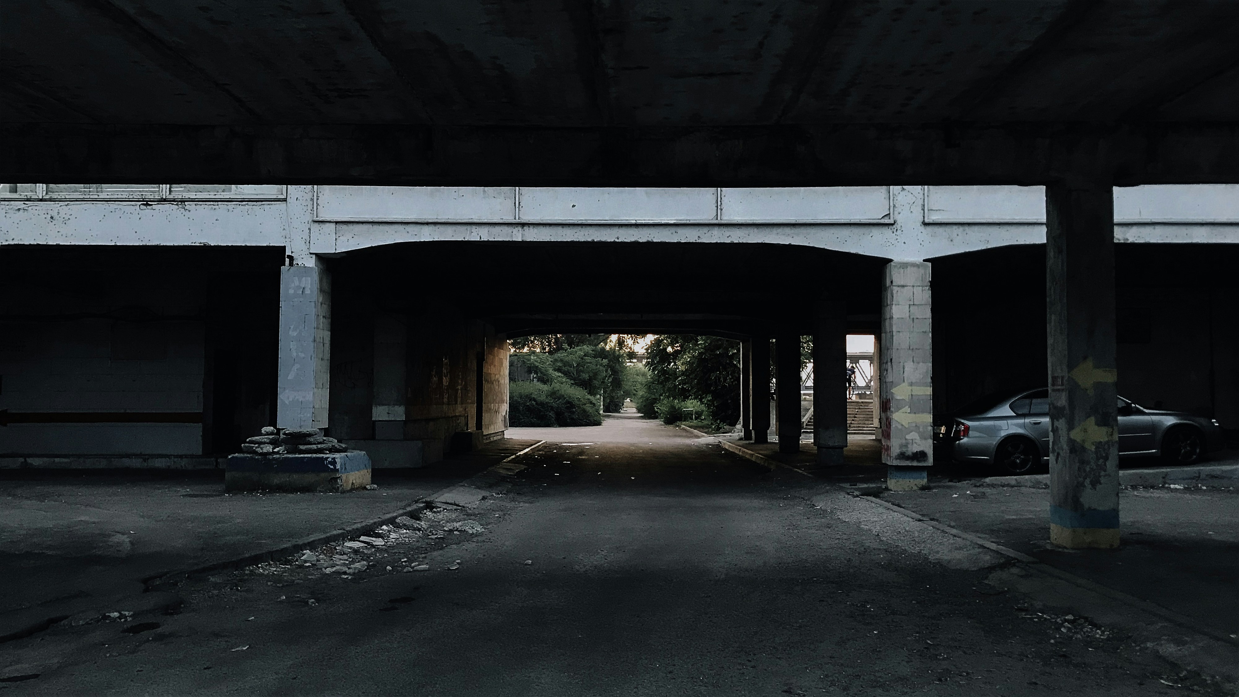 Dimly lit urban underpass with scattered debris and a glimpse of greenery in the distance.
