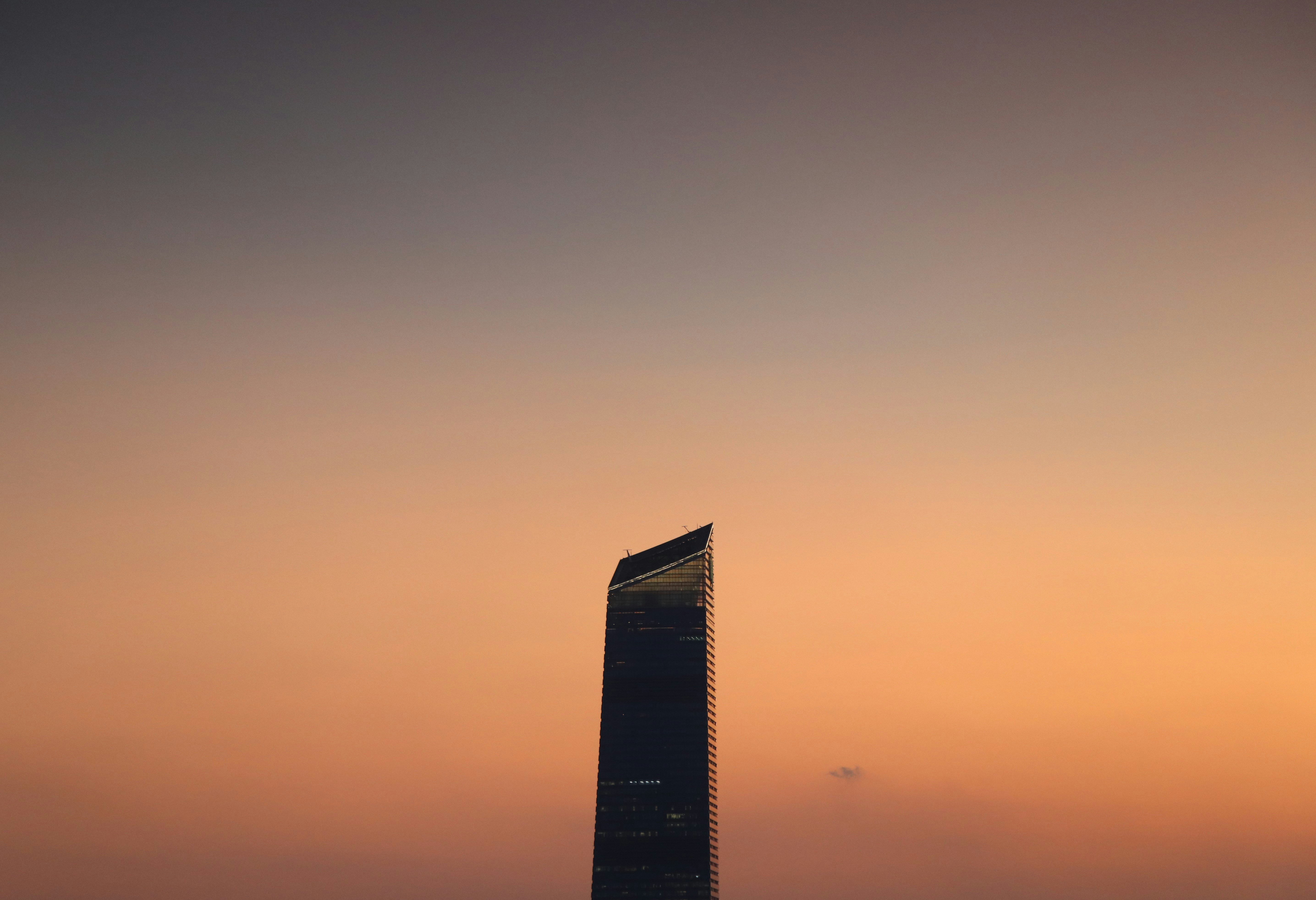 Tall skyscraper silhouetted against a gradient sunset, showcasing a blend of warm hues. The structure stands as a modern architectural marvel in the evening light.