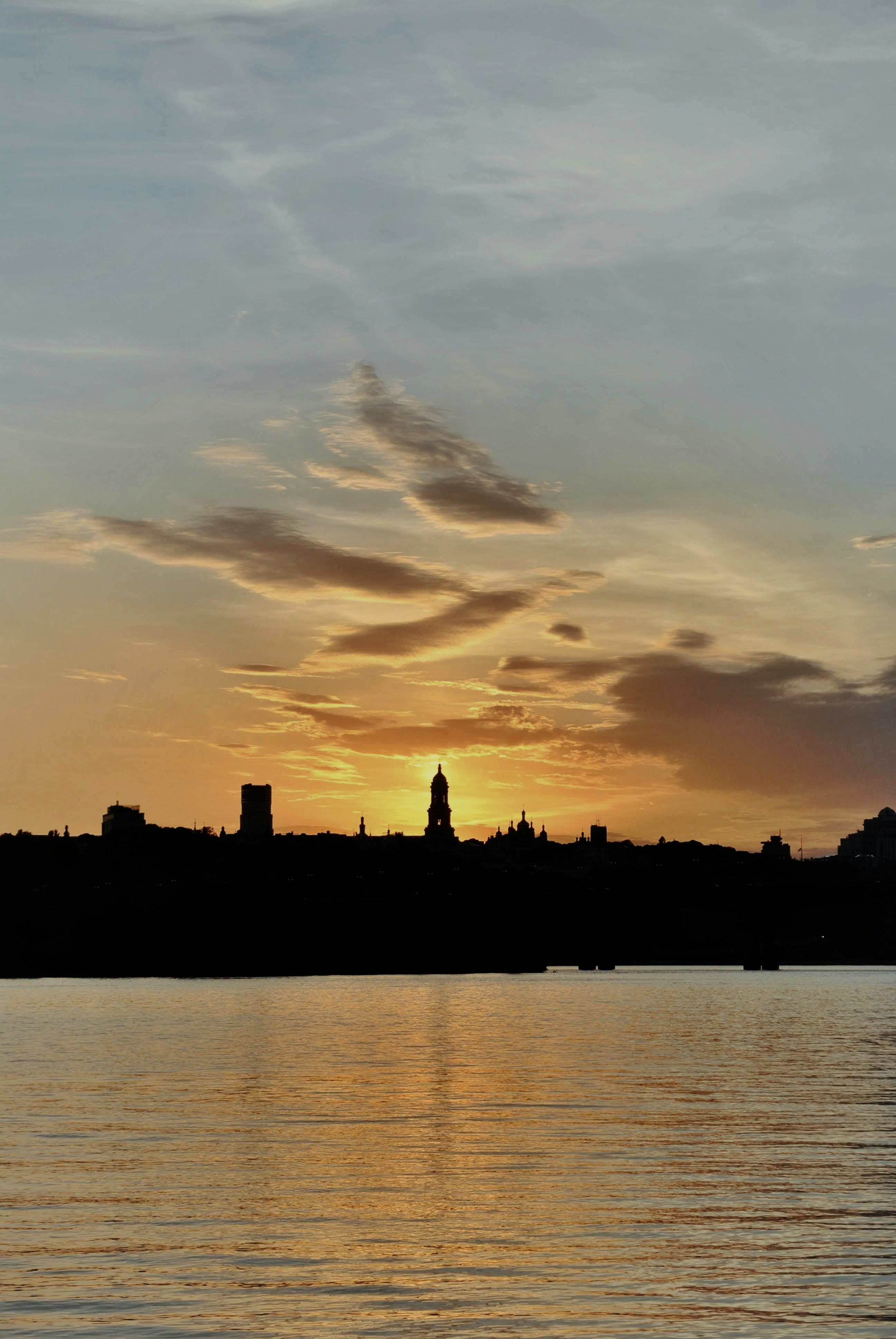 City skyline silhouetted against a vibrant sunset, reflecting on calm waters.