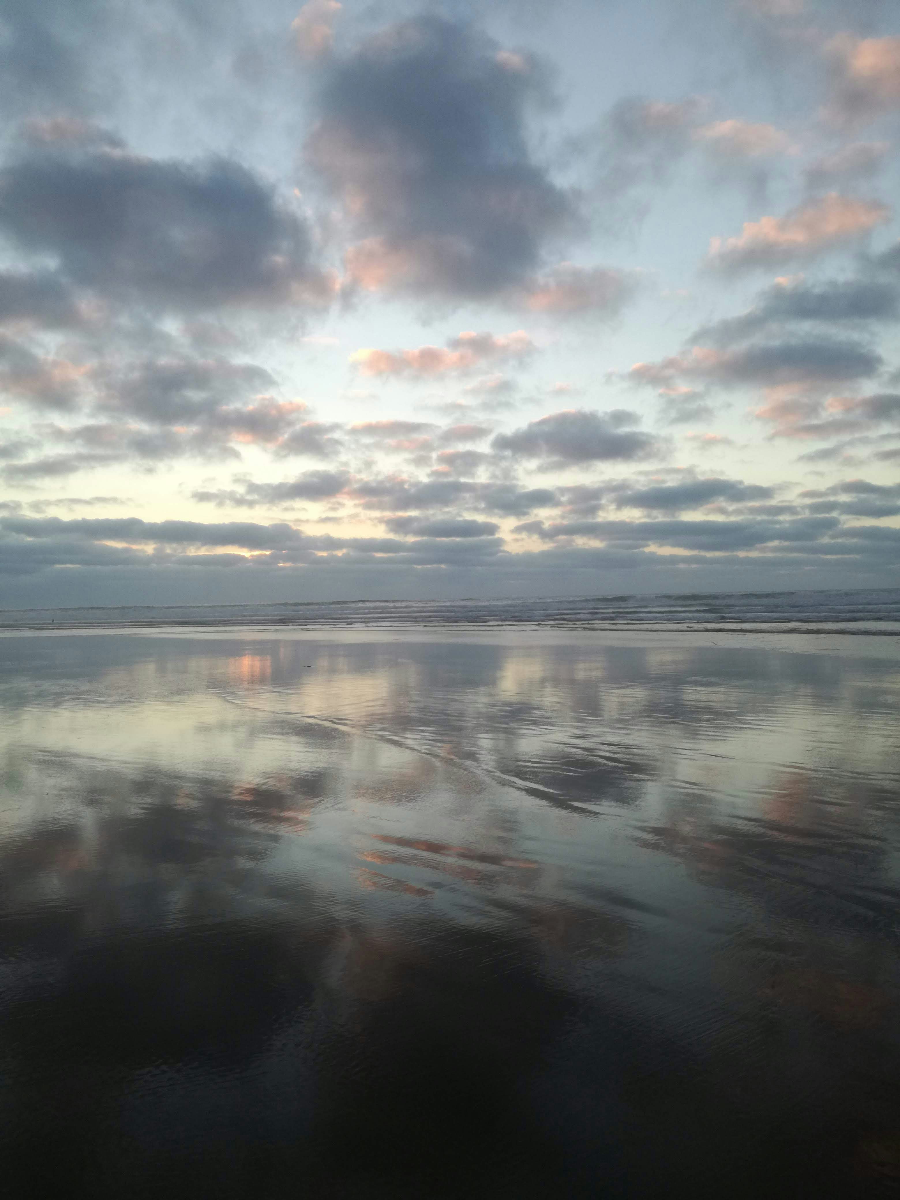 Clouds reflecting on a tranquil wet beach at dusk, creating a serene atmosphere.